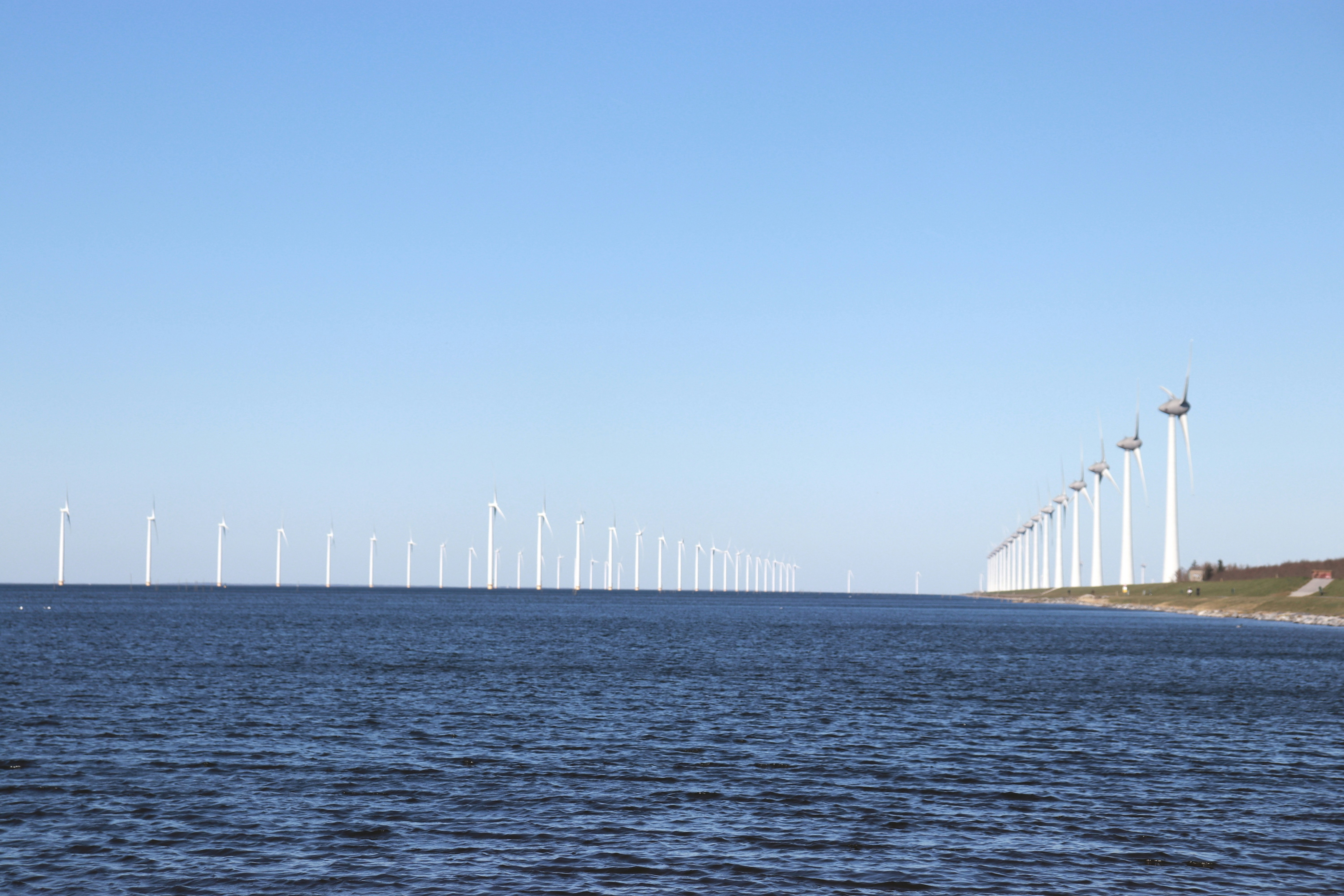 Wind turbines lining a coastal horizon under a clear blue sky.