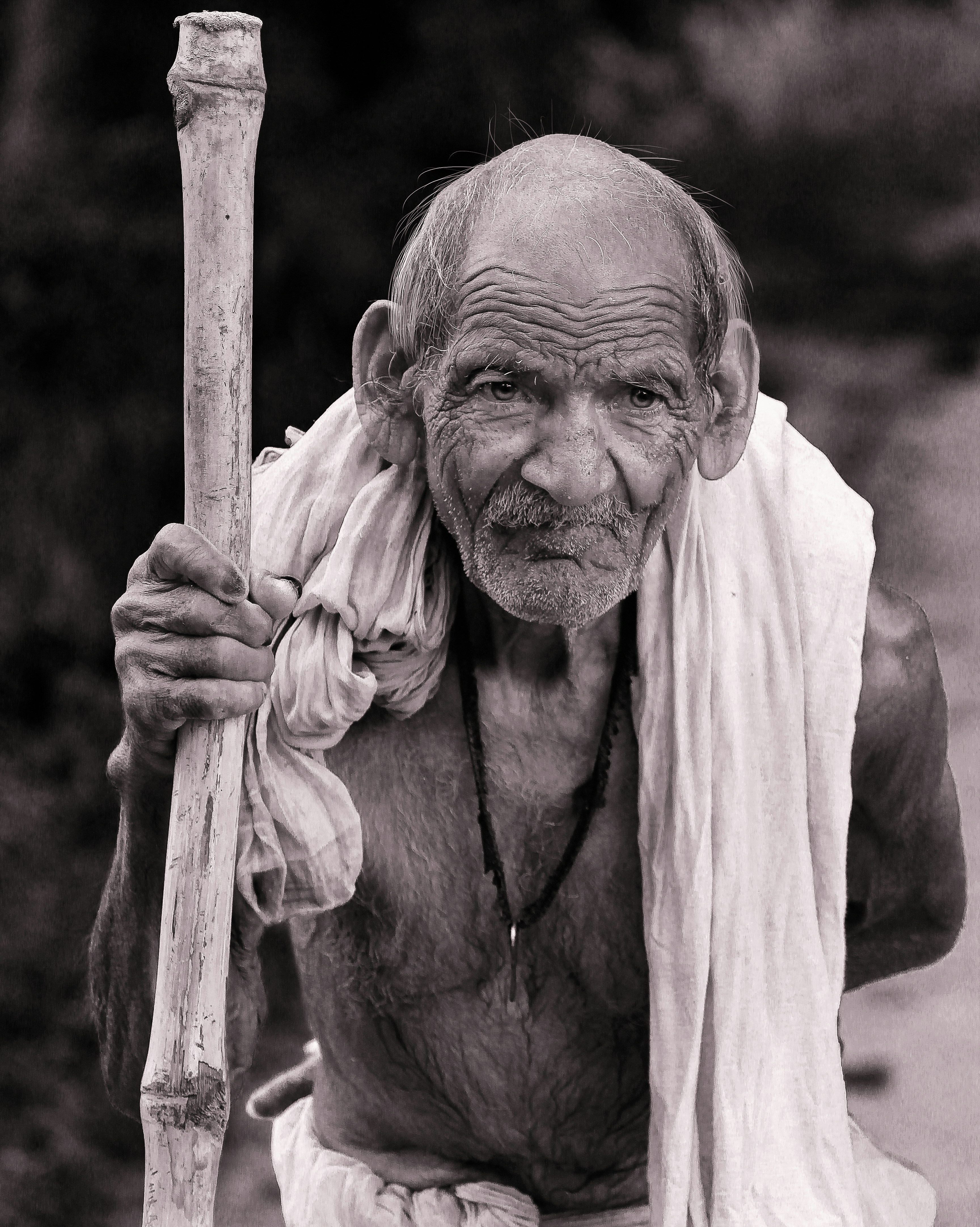 Elderly man holding a wooden staff, wrapped in a simple cloth, embodying resilience and life experience.