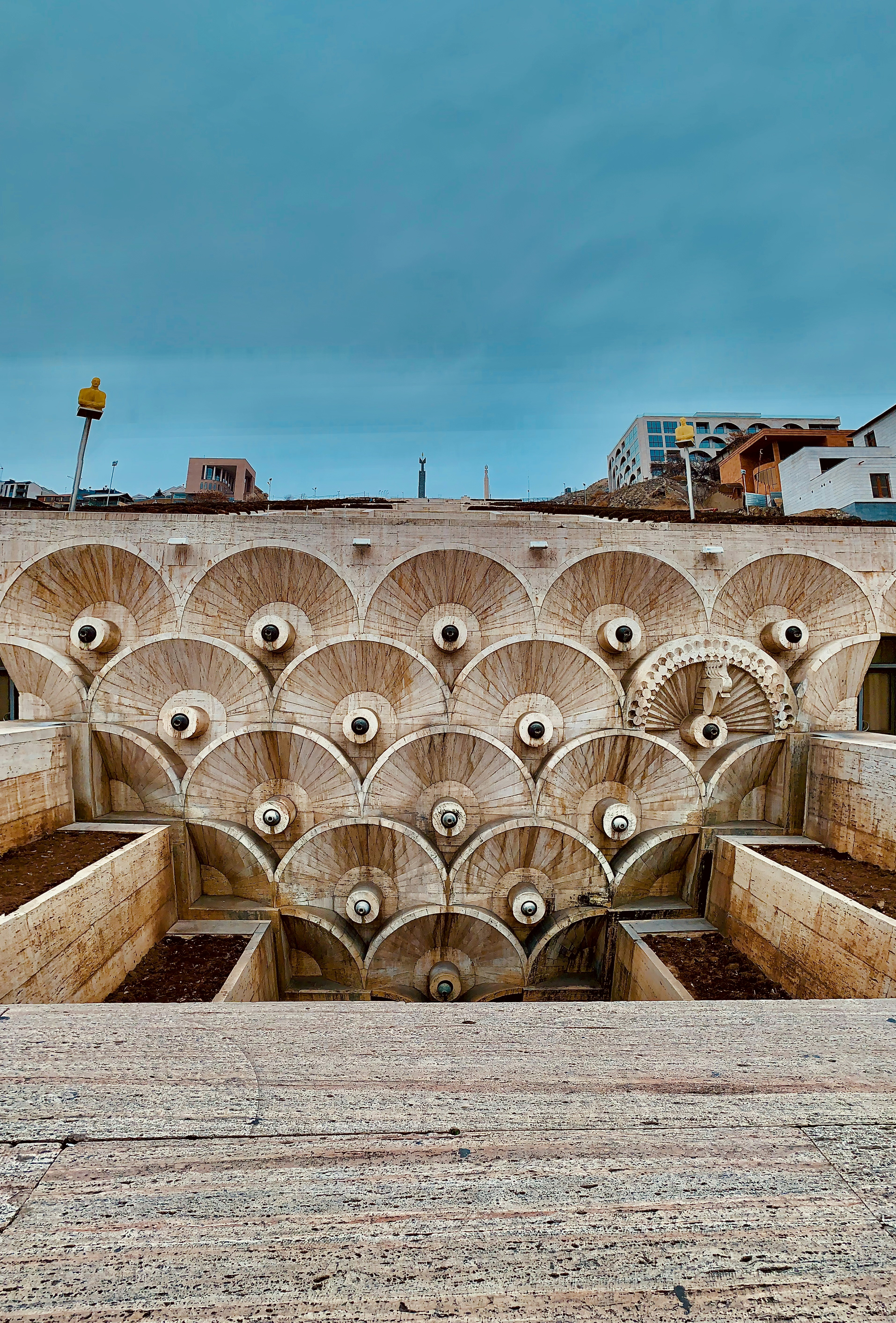 Intricate stone architecture featuring a series of curved elements and water features, showcasing modern design against a cloudy sky.