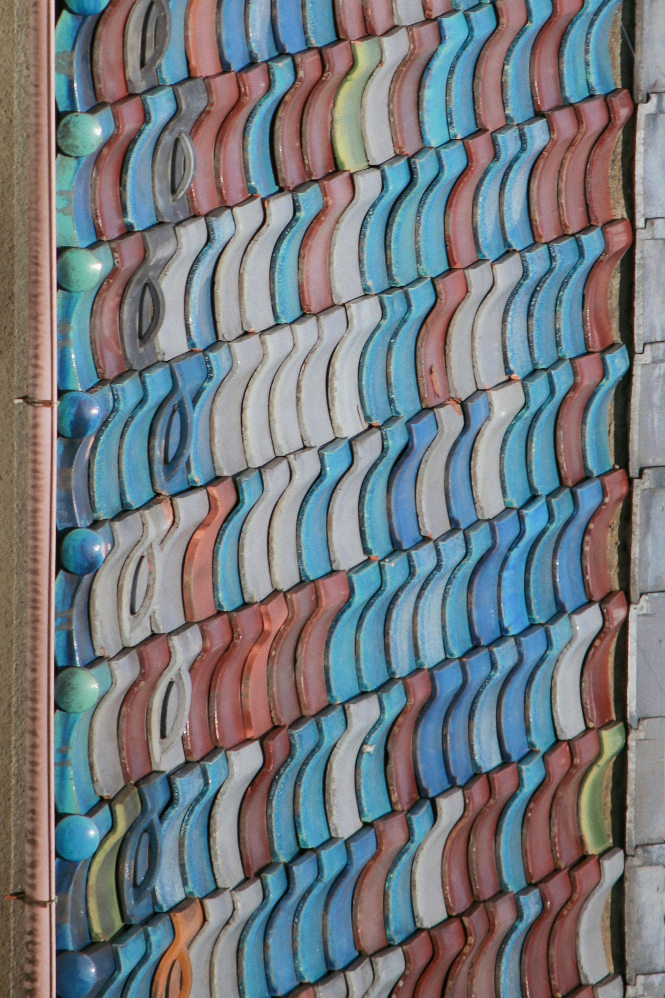 Colorful ceramic tiles arranged in a wavy pattern, creating a dynamic visual texture on a building facade.