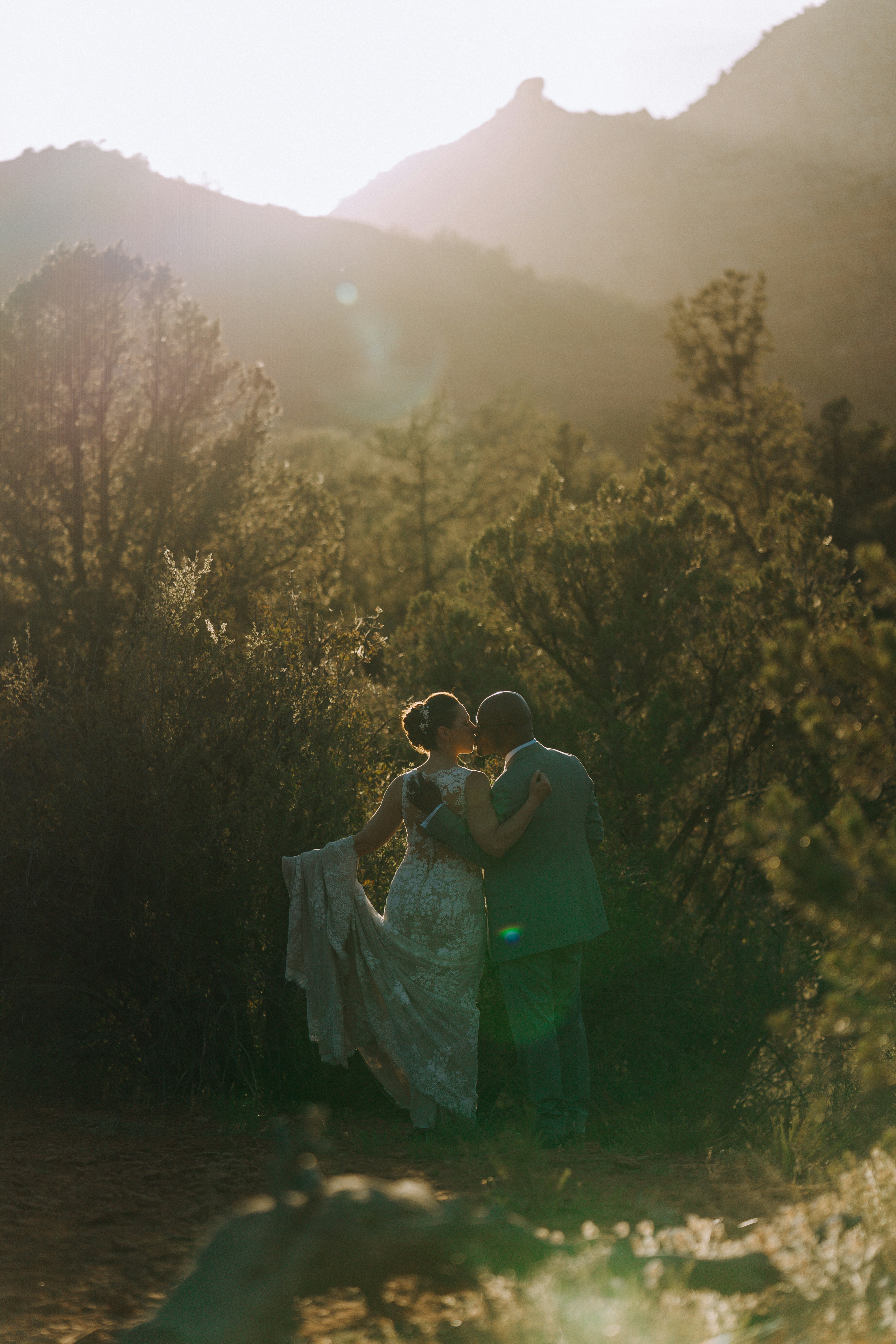 Couple sharing an intimate moment surrounded by lush greenery and mountains during golden hour.