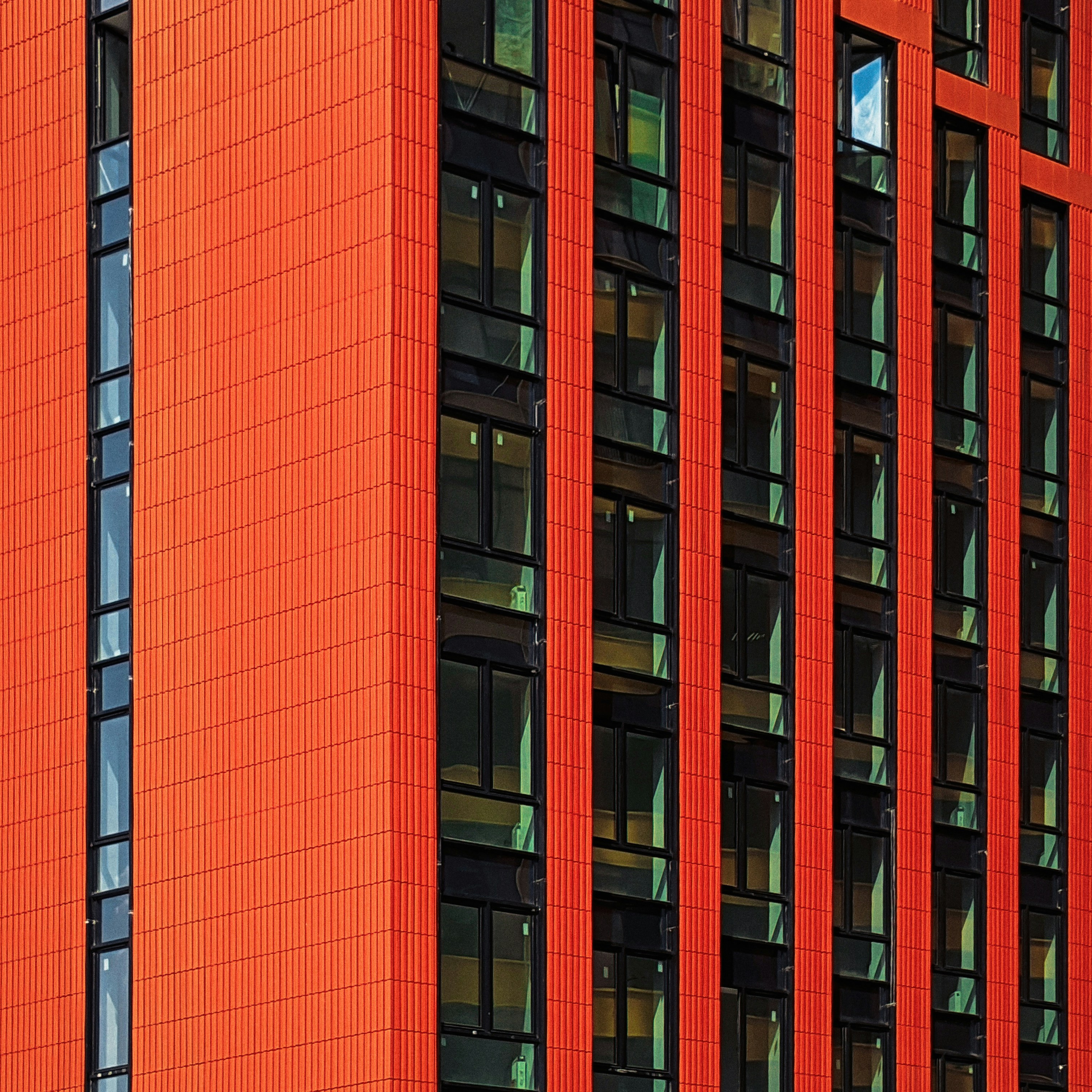 Vibrant orange facade of a modern building juxtaposed with reflective glass windows, showcasing contemporary architectural design.