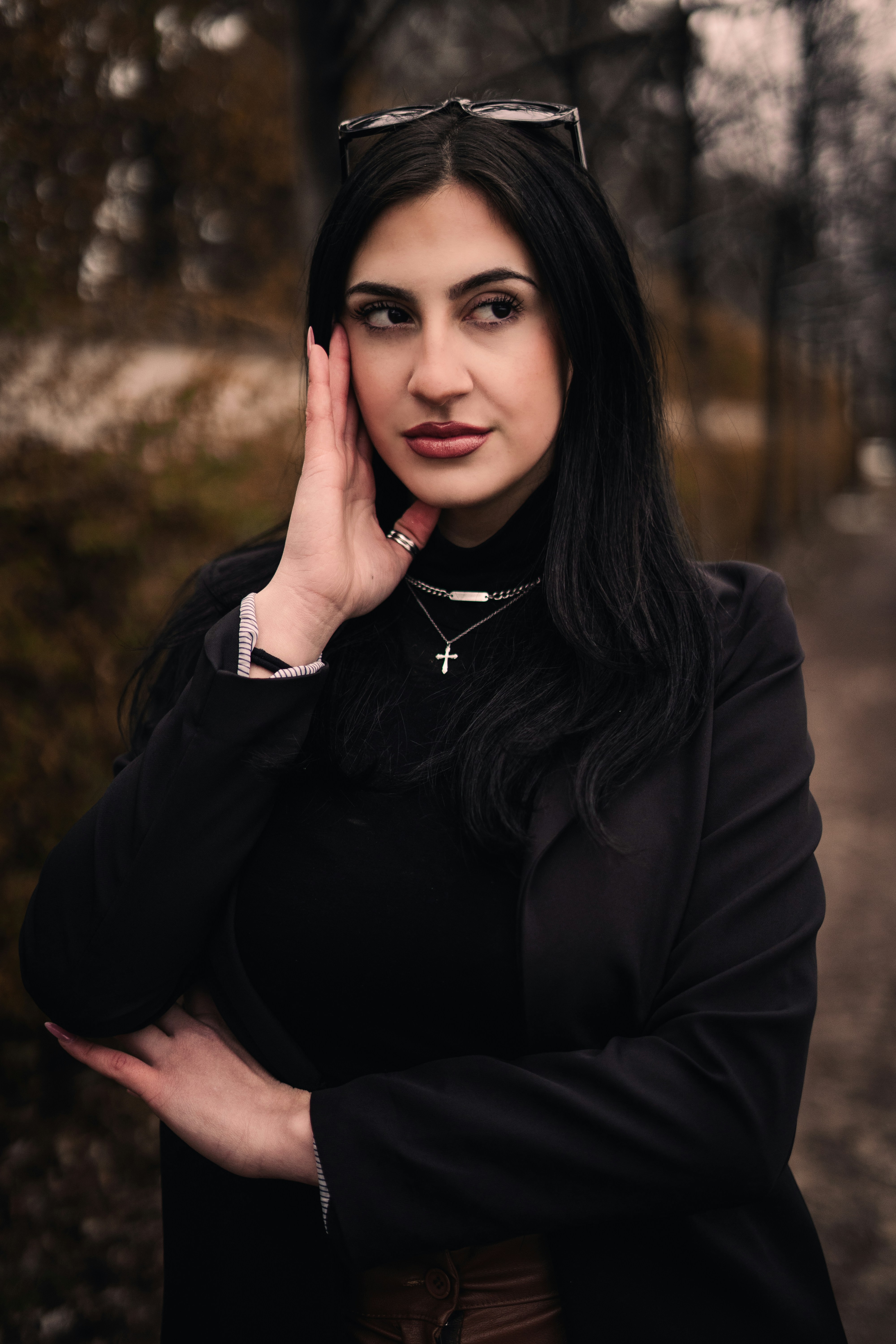 A woman in a black blazer thoughtfully resting her hand on her cheek, surrounded by a blurred, autumnal pathway. Her expression conveys a sense of introspection.