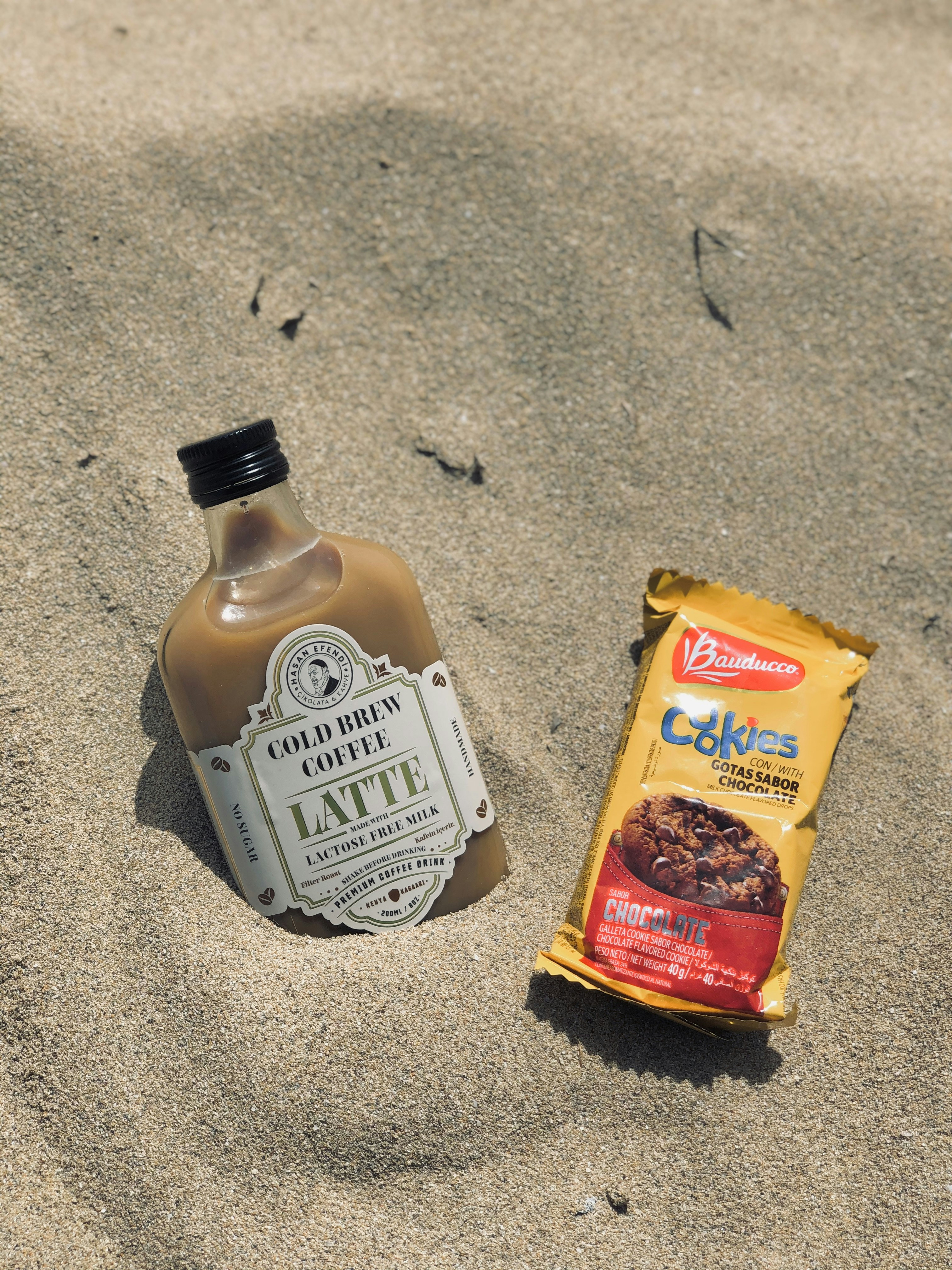 Beachside Duo: Latte Bottle and Bauducco Cookie Rest on Sunlit Sand