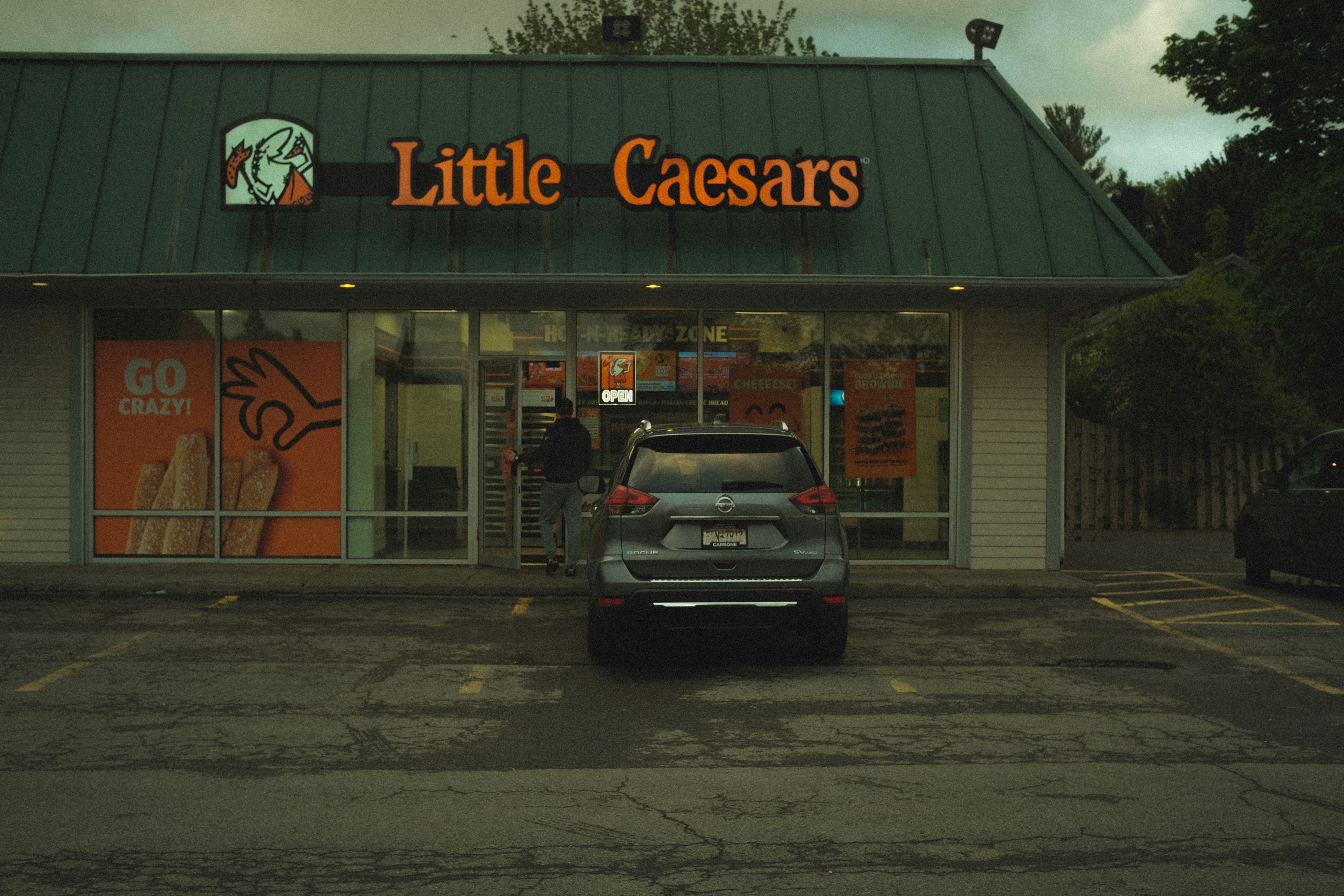 Parking Lot Interlude at Little Caesars: A Silver SUV Framed by Neon Orange Sign