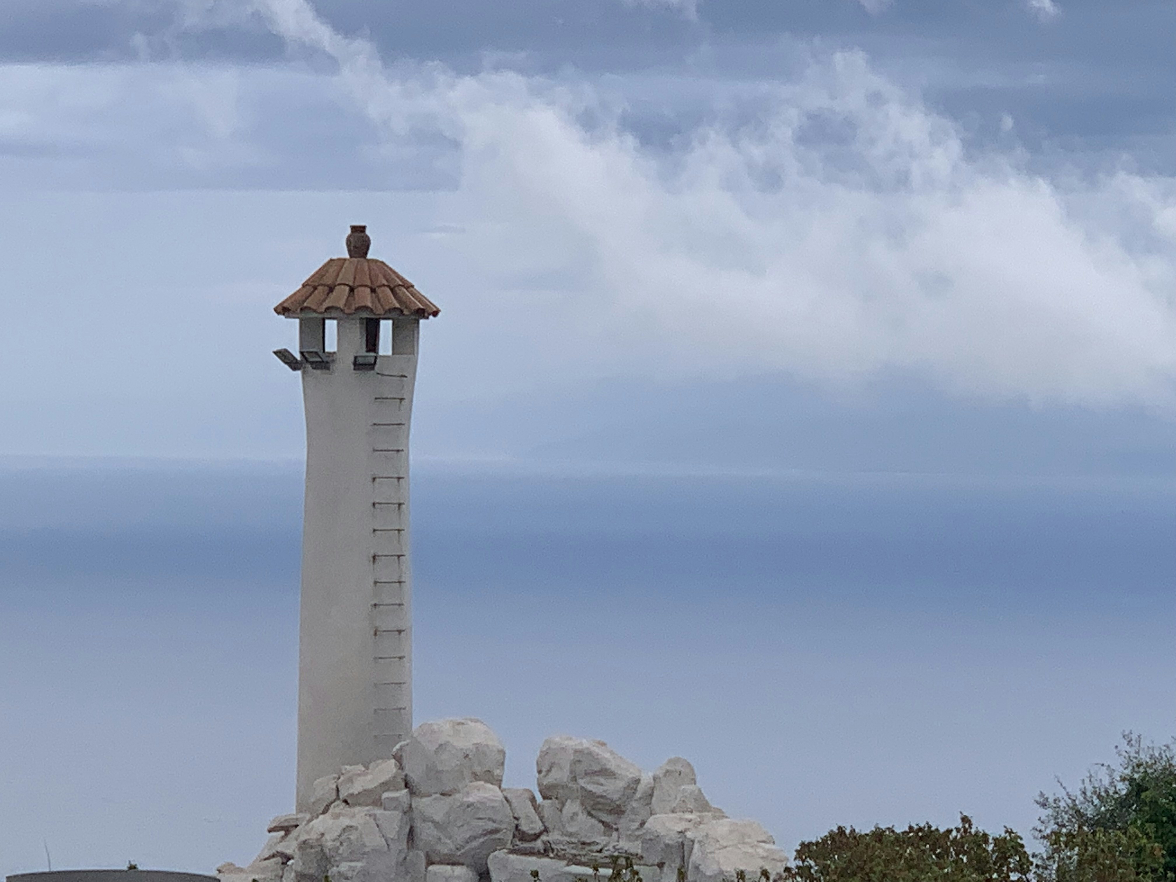A lighthouse stands tall amidst rocky terrain under a cloudy sky, symbolizing guidance and safety for passing ships.