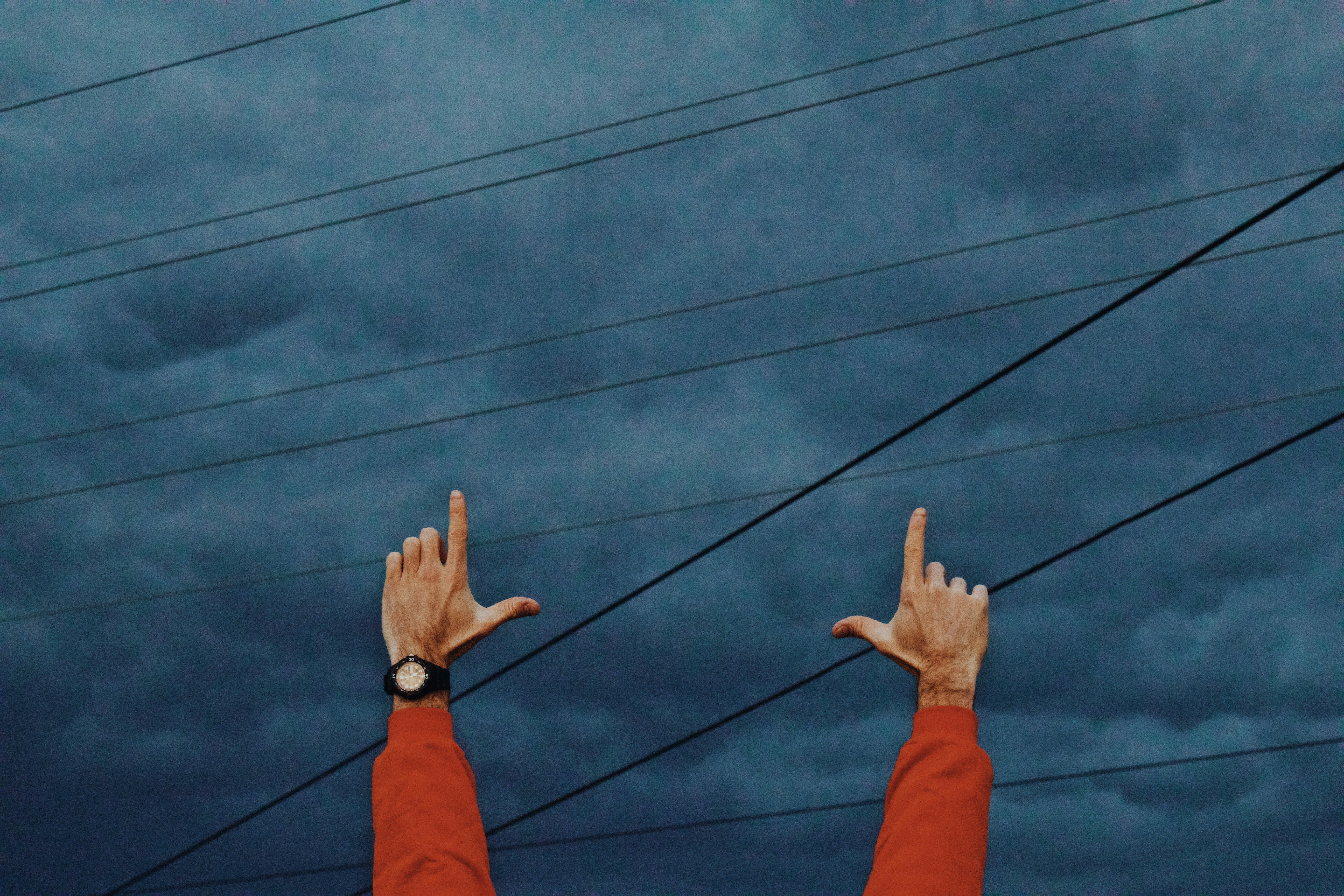 Signals to the Storm: Orange Sleeves Reach Toward a Crisscrossed Sky
