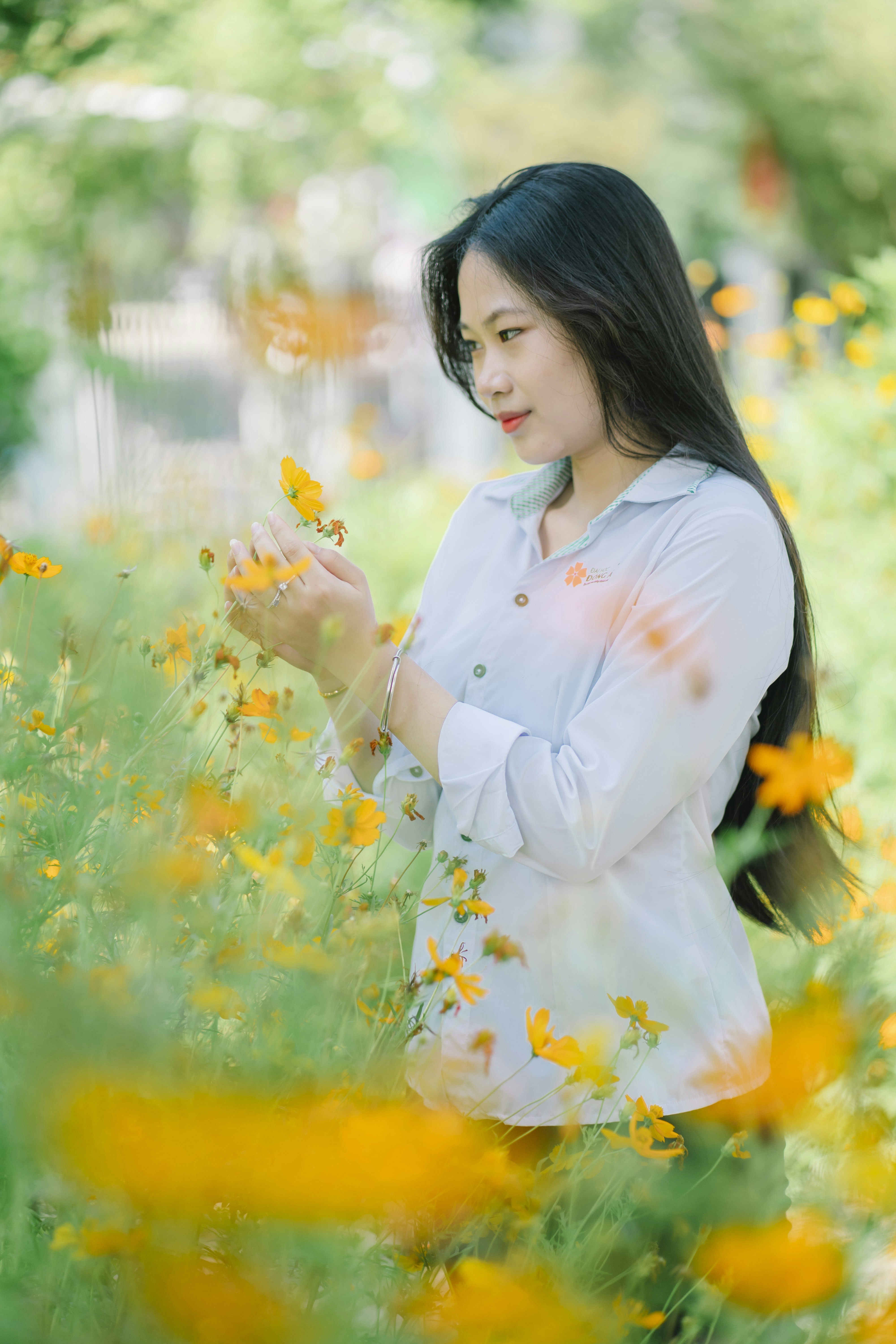 A woman gently caresses wildflowers in a vibrant garden, surrounded by a sea of yellow blooms. The soft focus adds a dreamy quality to the scene.