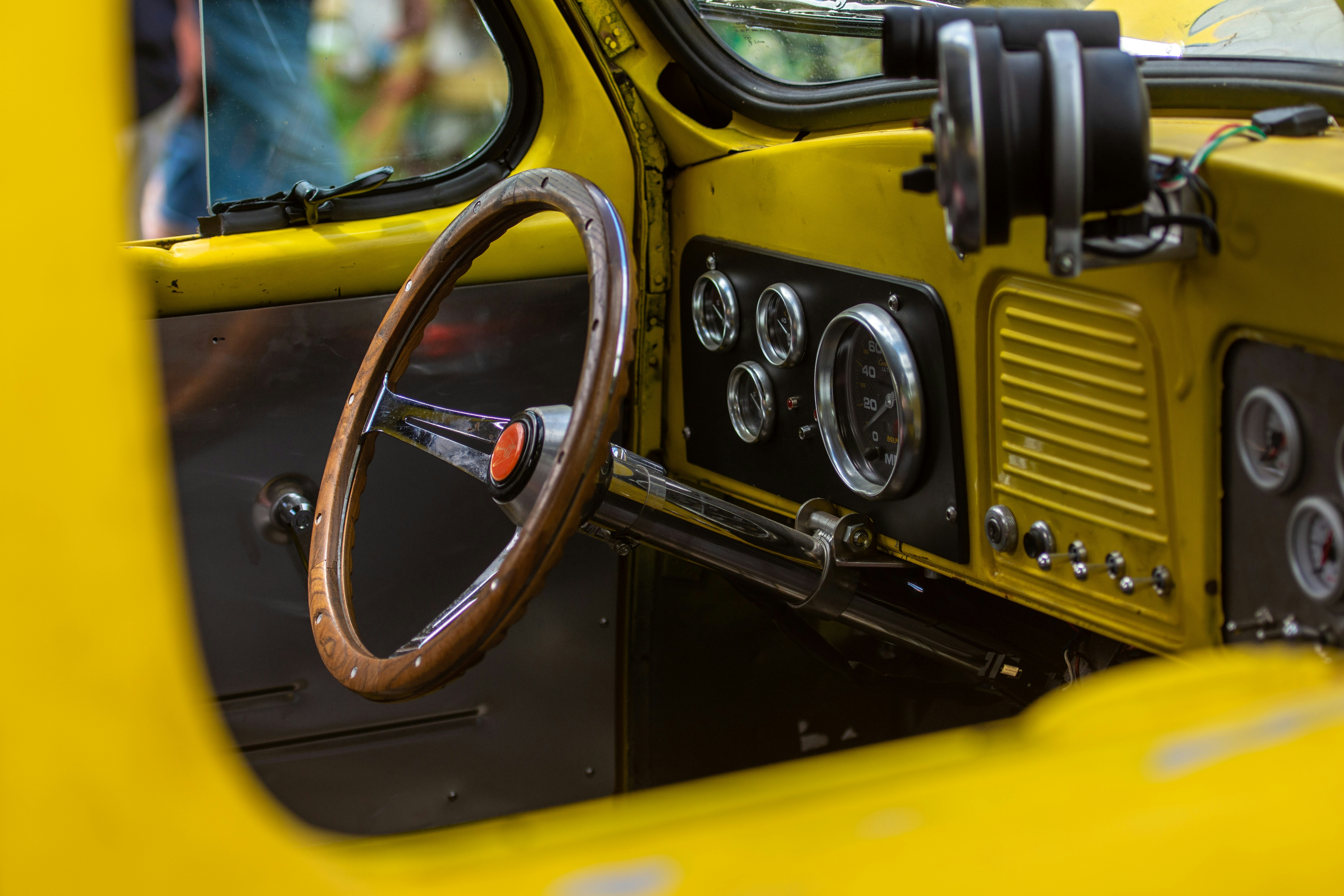 Interior view of a classic yellow vehicle showcasing a wooden steering wheel and vintage gauges. The nostalgic design evokes memories of a bygone era.