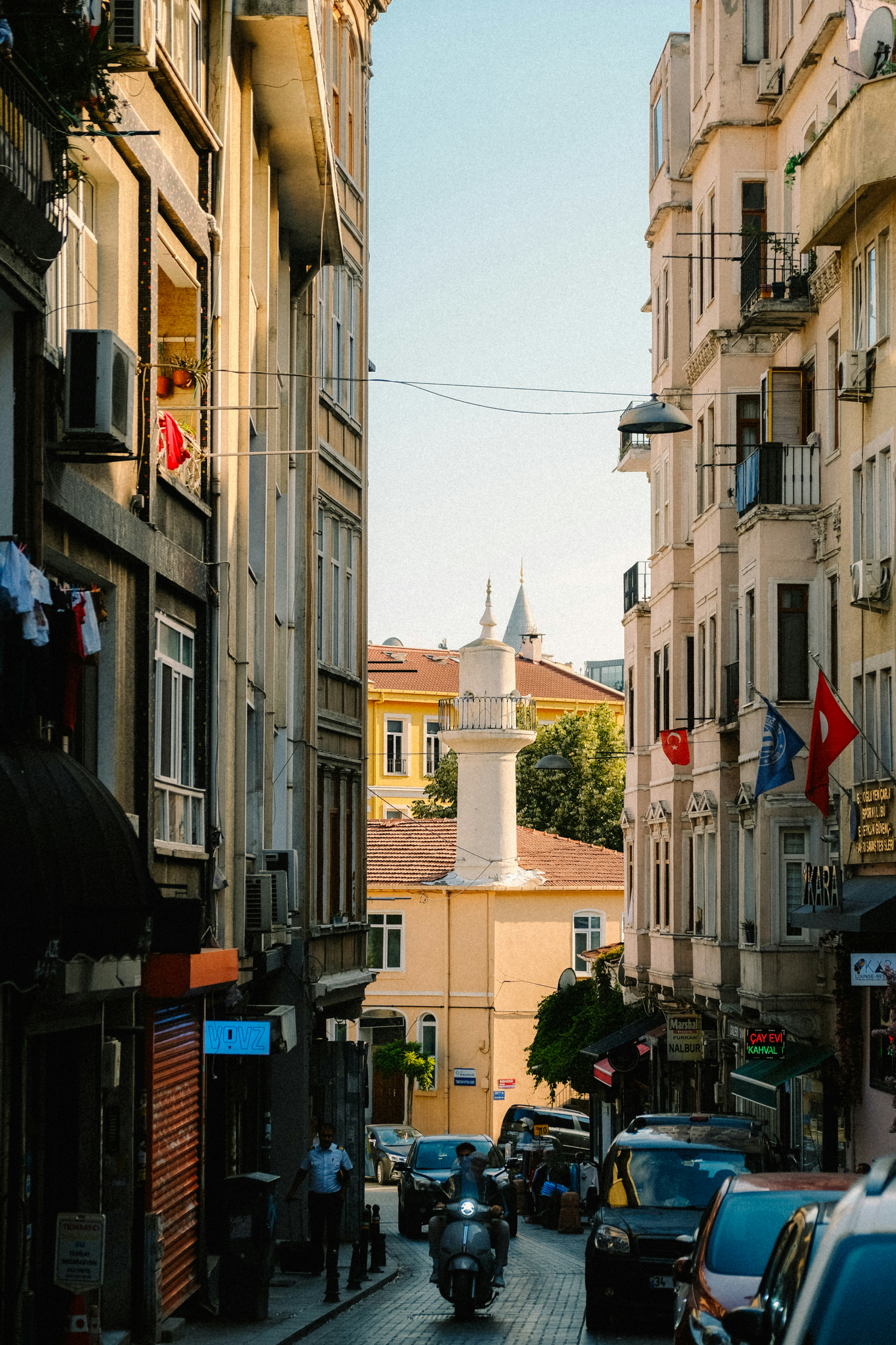 Narrow street flanked by historic buildings, revealing a white minaret against a vibrant backdrop of city life.