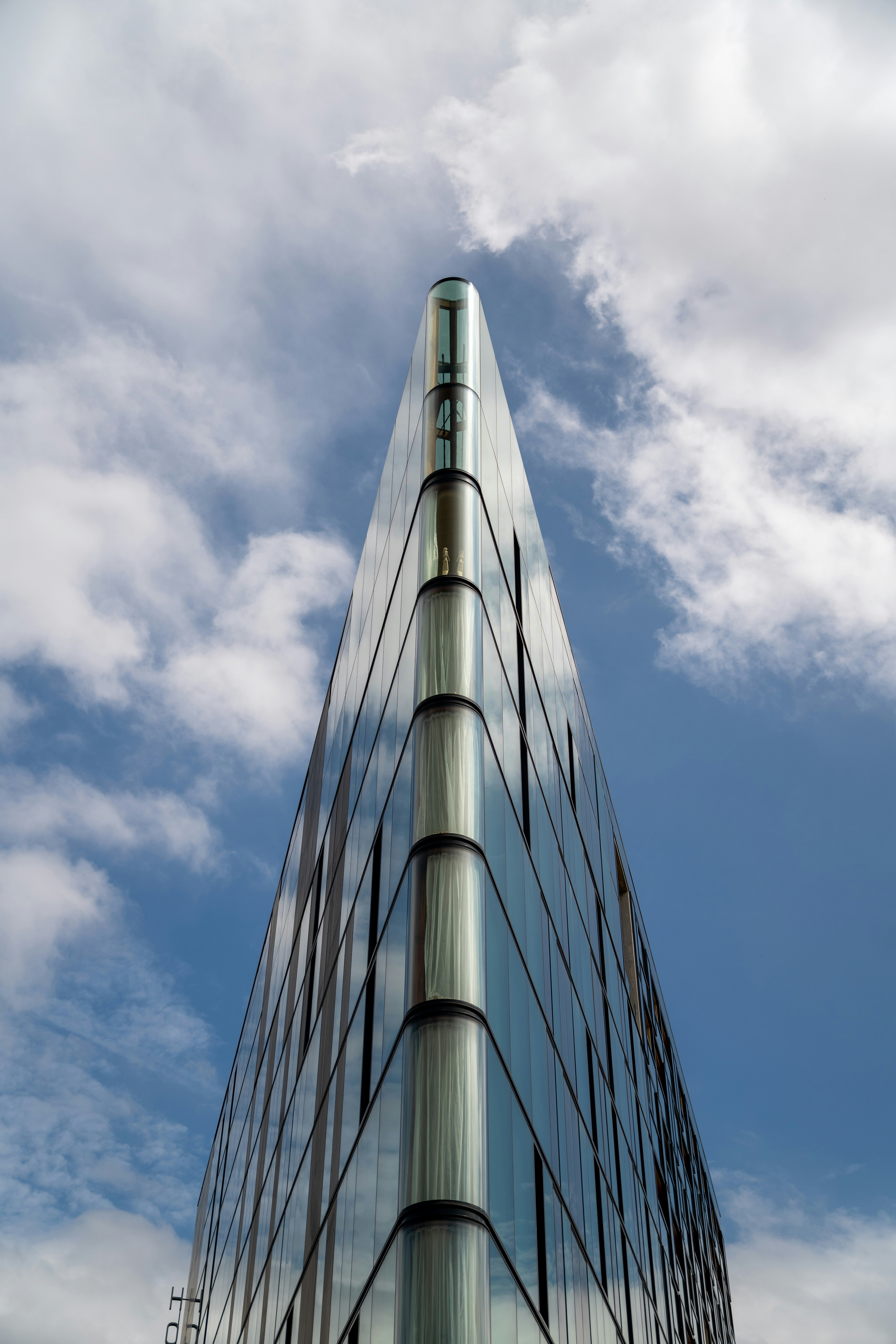 Sleek glass building reaching towards the sky, reflecting clouds and blue hues. A testament to contemporary design.