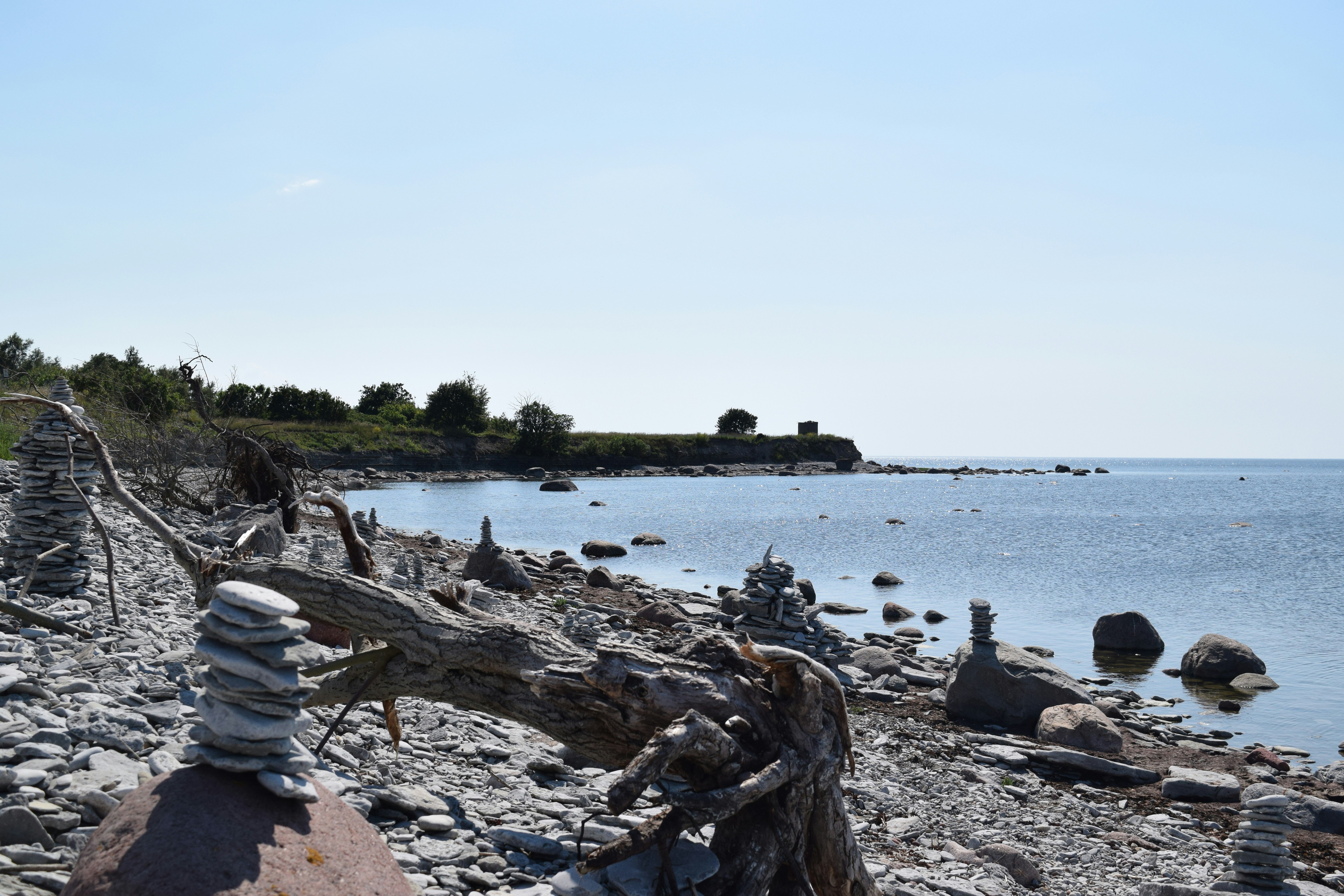 Stone Cairns at the Quiet Edge: A Pebbled Shore Framed by a Distant Fortress