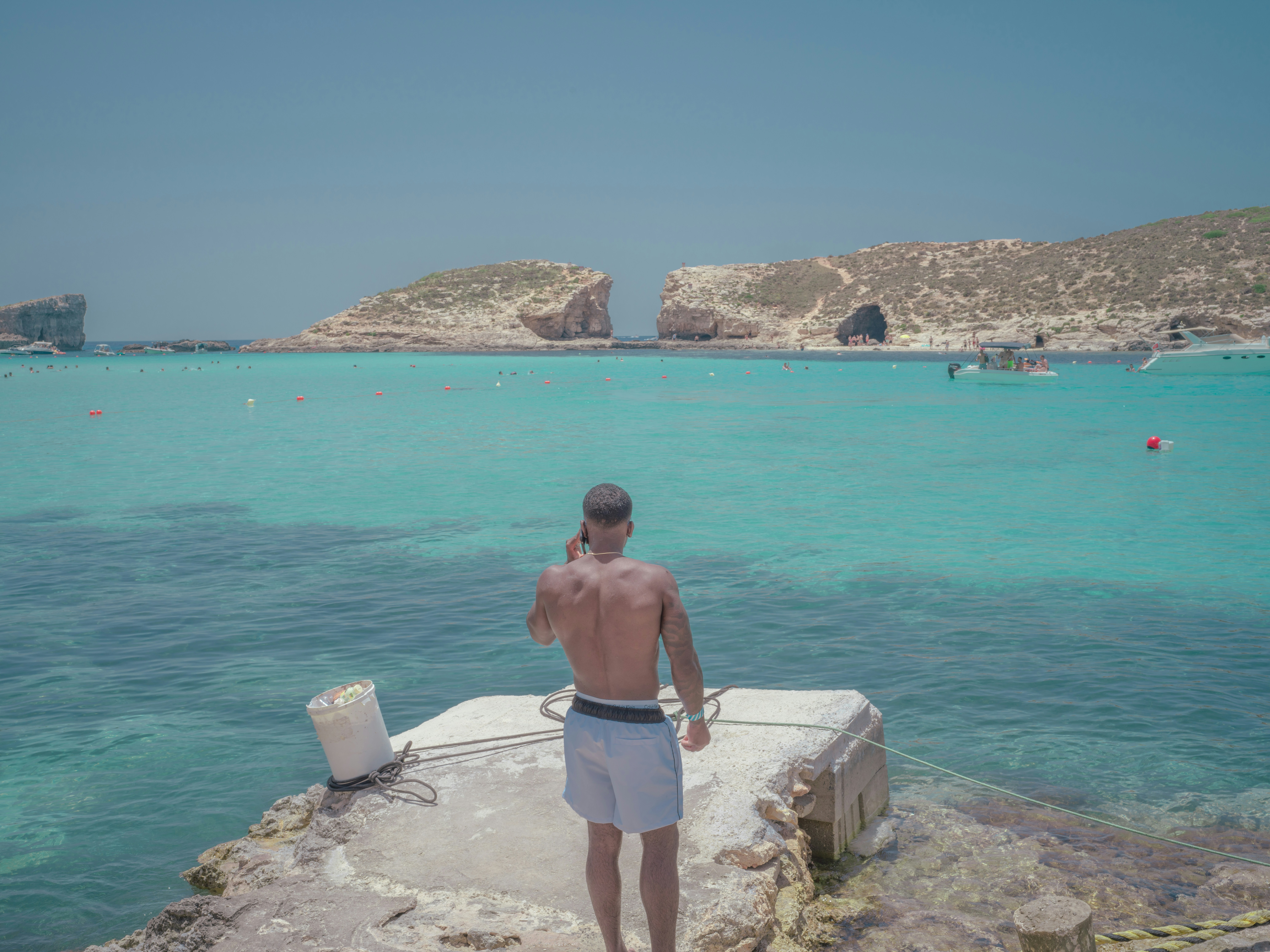 Turquoise Threshold: A solitary figure on a sunlit jetty gazes toward emerald seas