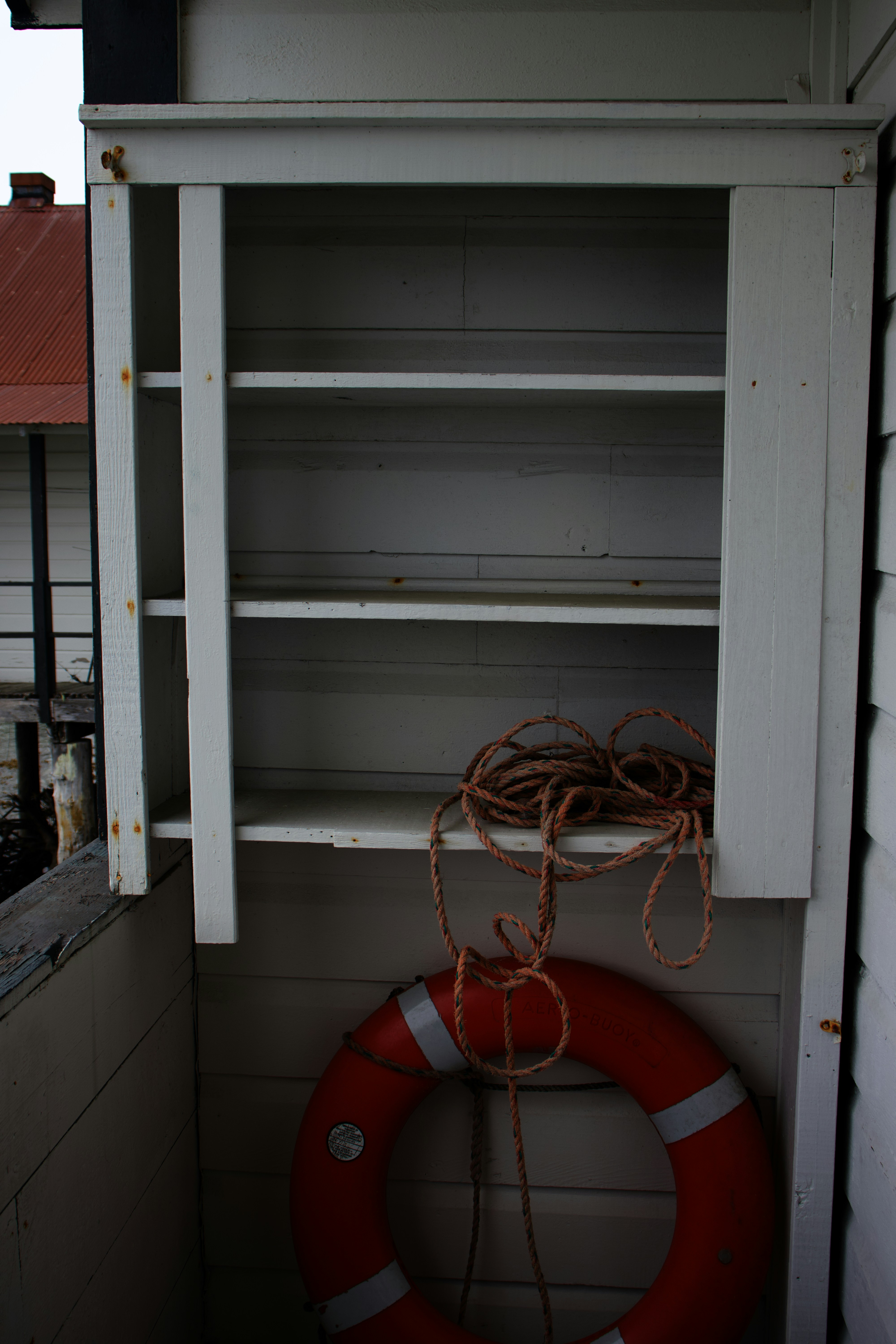 Orange Lifebuoy Anchors a Quiet Porch: White Shelving, Rope, and Weathered Wood