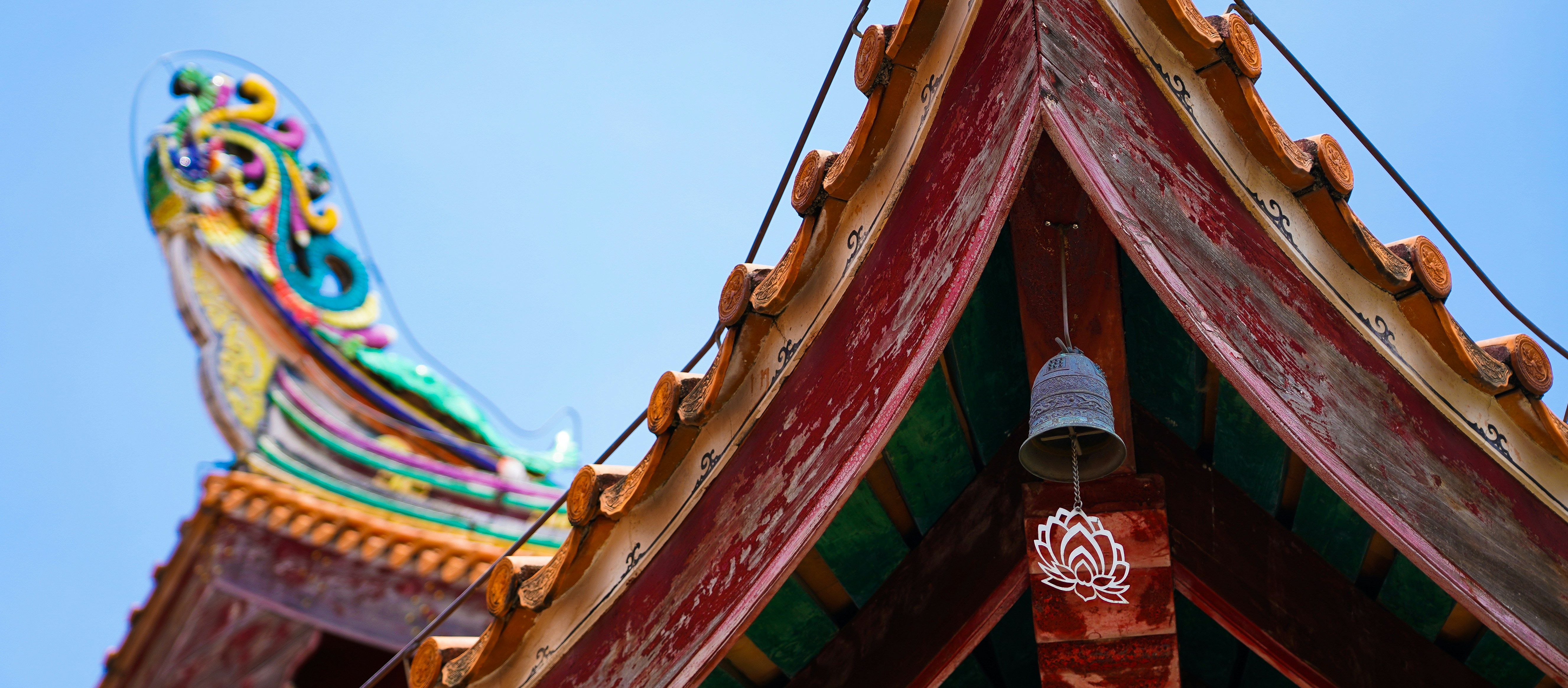 Intricate dragon sculpture atop a traditional roof with vibrant colors against a clear blue sky.