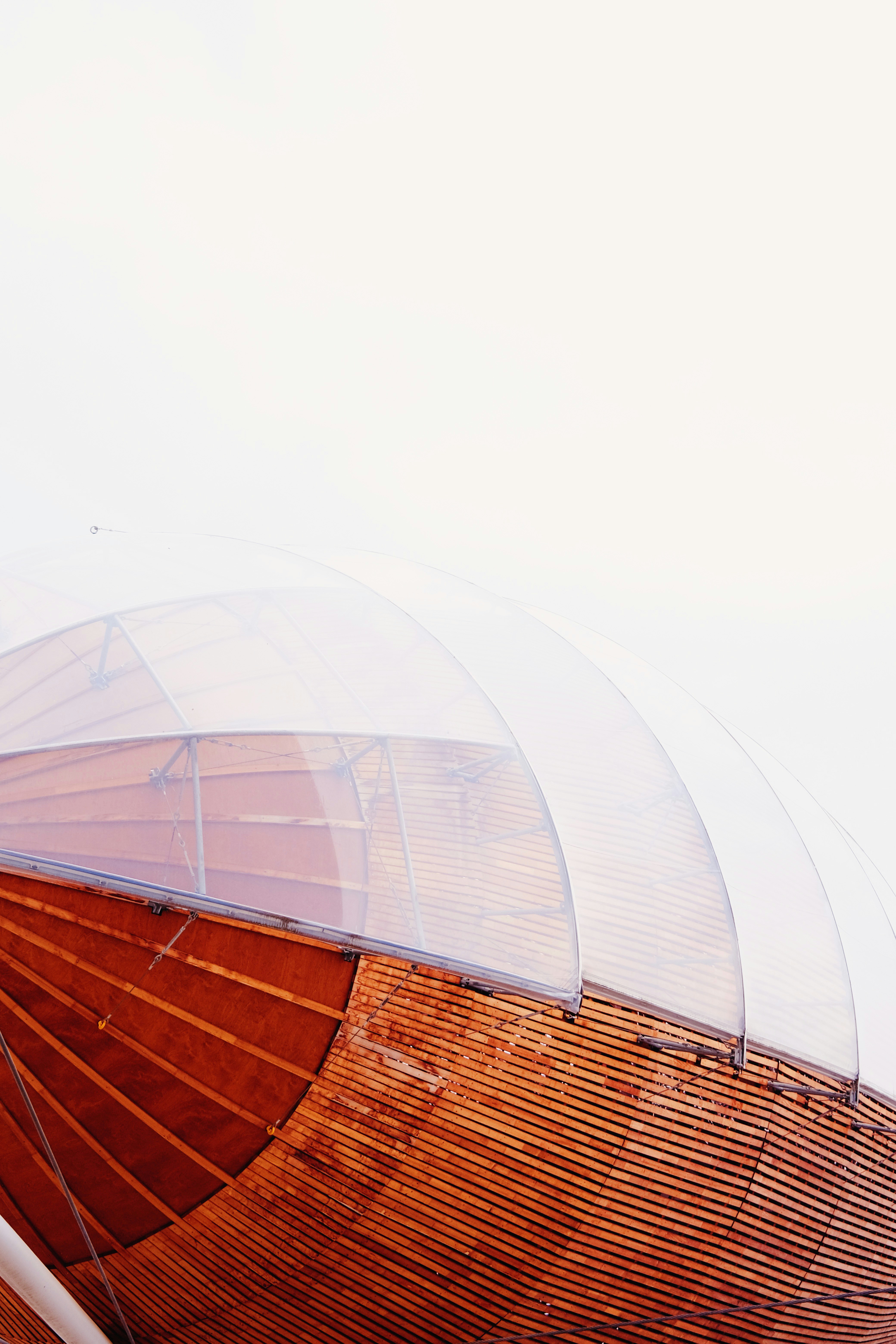 Curved wooden structure beneath a translucent canopy against a bright sky.
