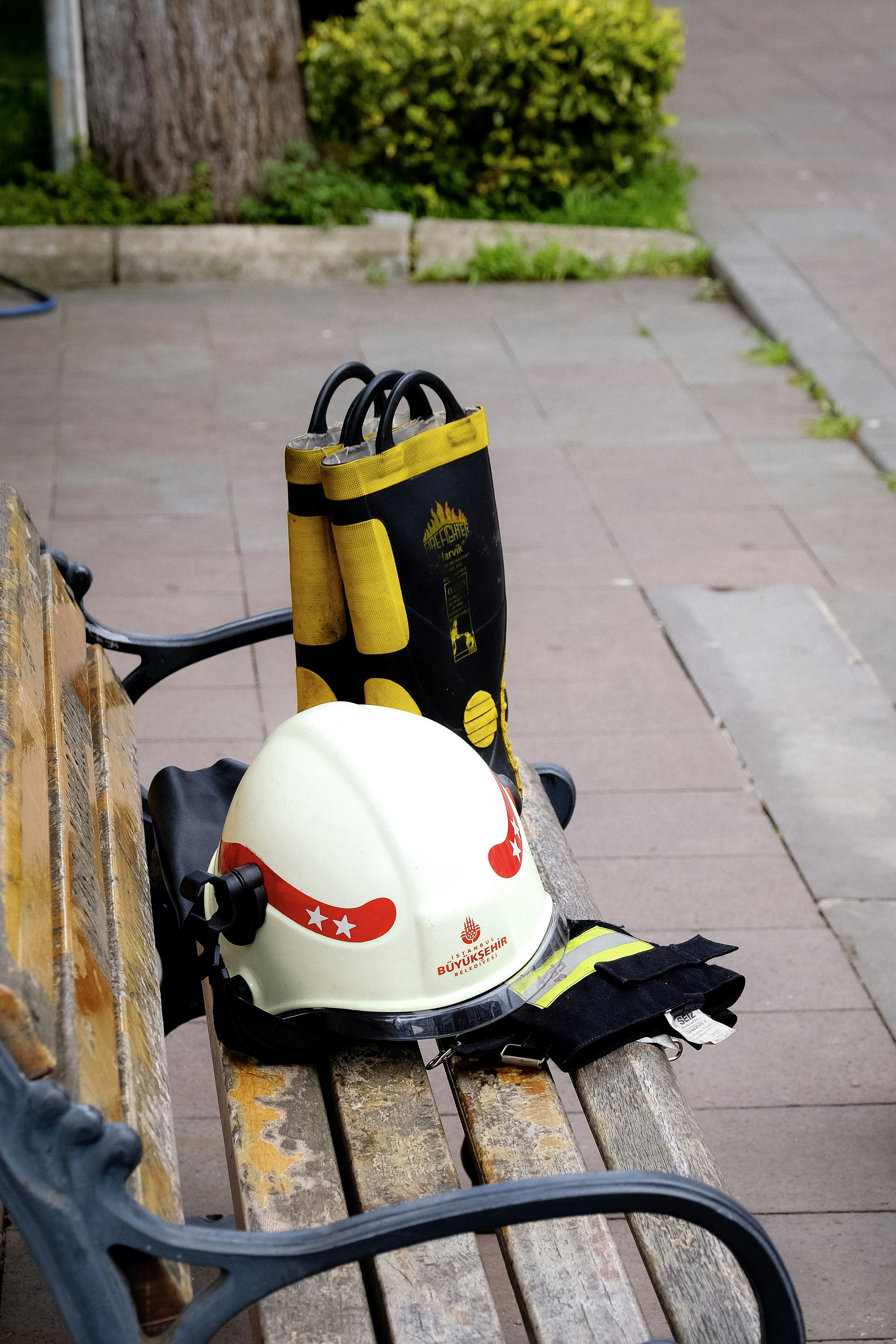 Benchside Sentinel: White hard hat resting beside a yellow-and-black bag on a weathered park bench.