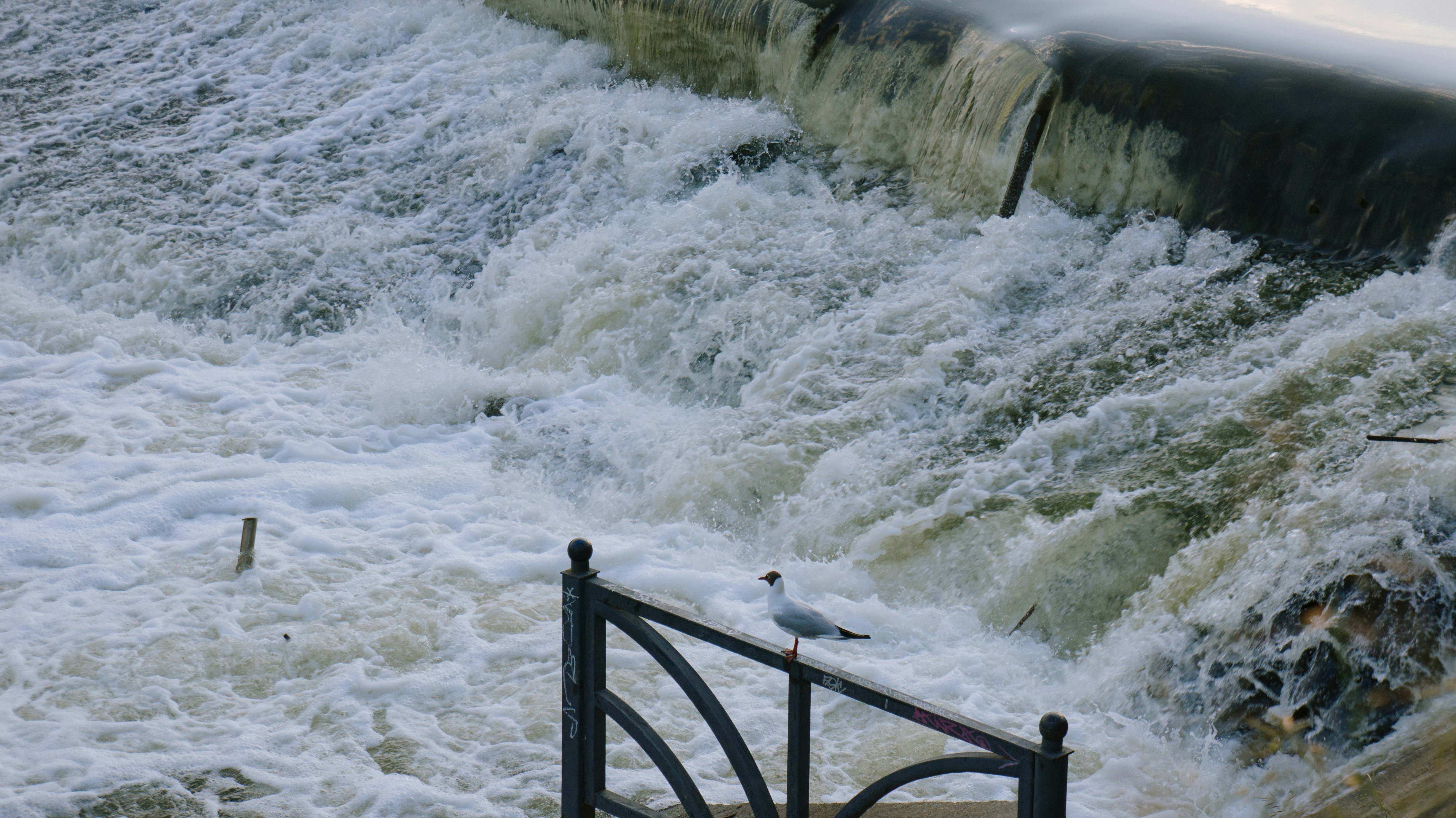 A river with a railing and a railing with a large waterfall photo ...