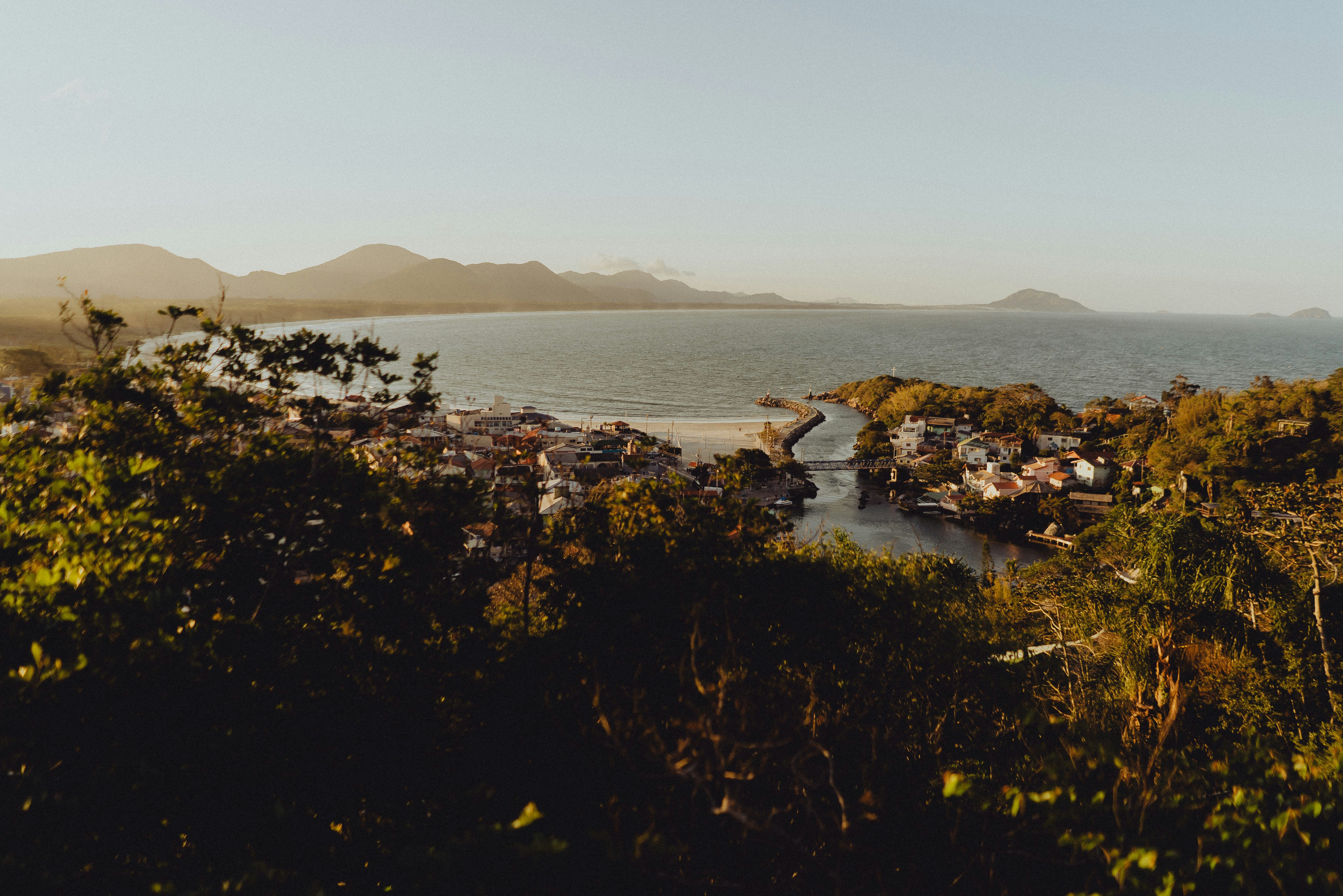 Coastal village nestled between lush greenery and tranquil waters, showcasing a winding river leading to the sea. The scene captures the harmony of nature and human habitation.