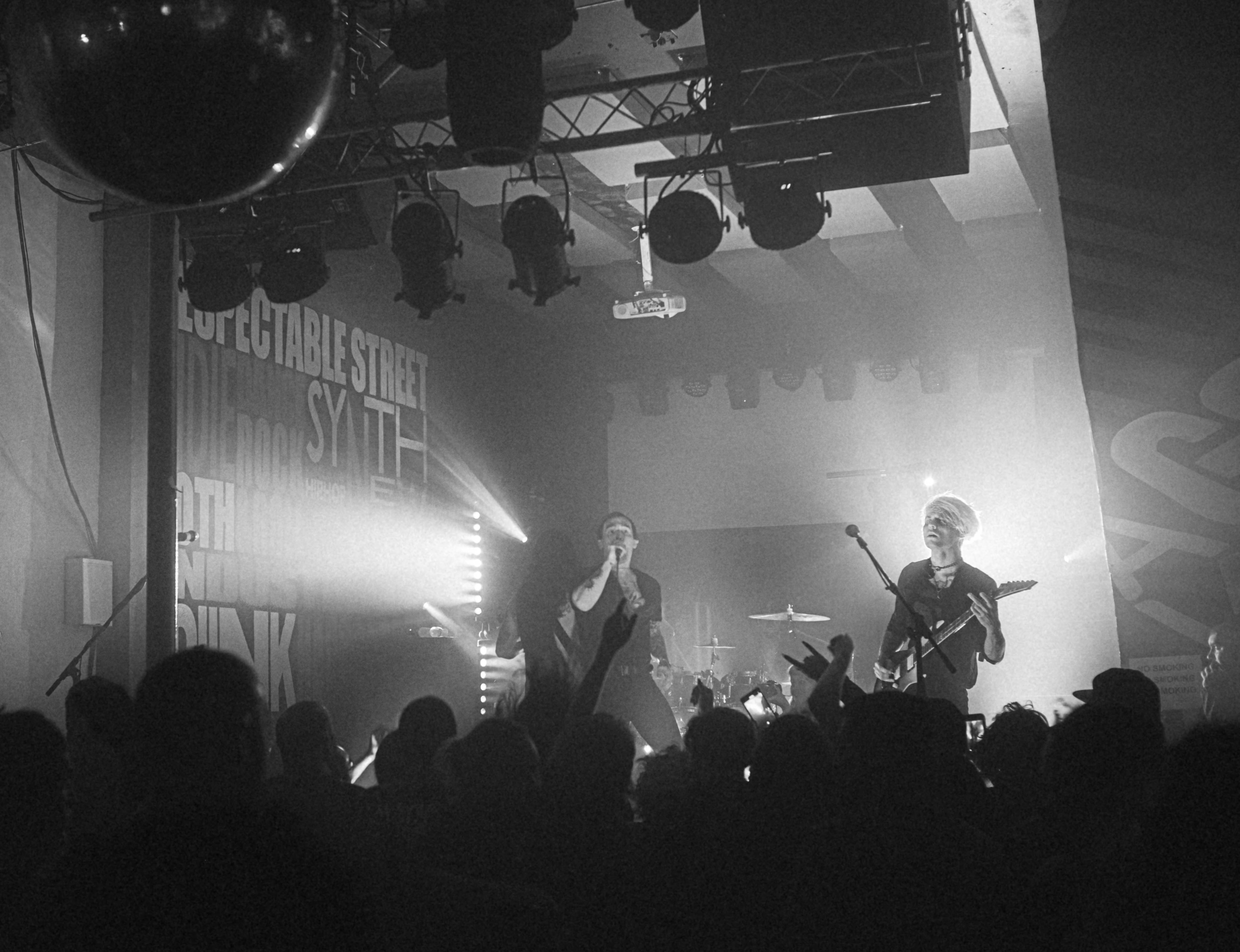 Live performance by a band on stage, illuminated by dramatic lighting, with an audience immersed in the experience.