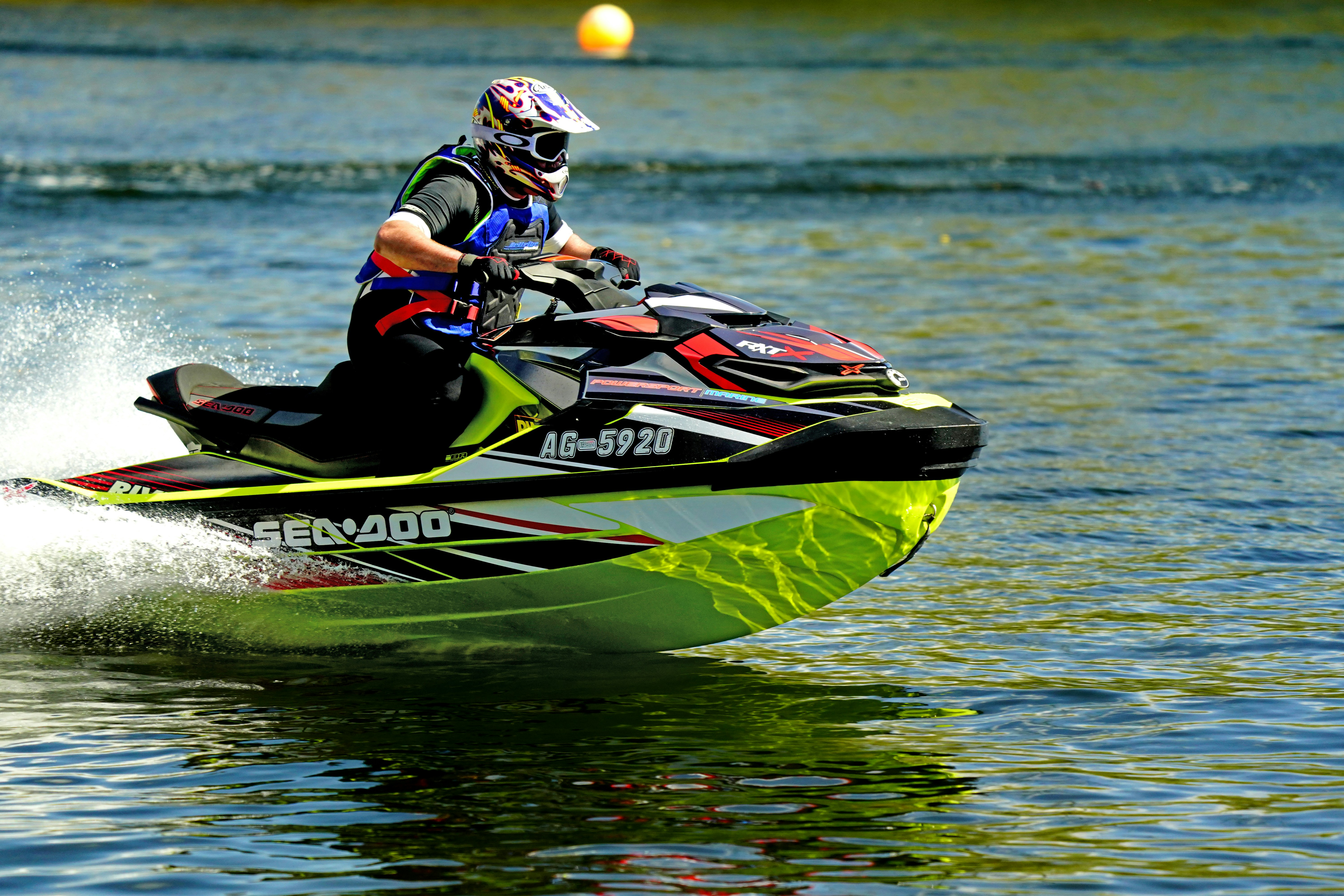 A jet ski rider skillfully maneuvers across a shimmering body of water, creating dynamic splashes as they accelerate. The vibrant colors of the watercraft stand out against the serene backdrop.