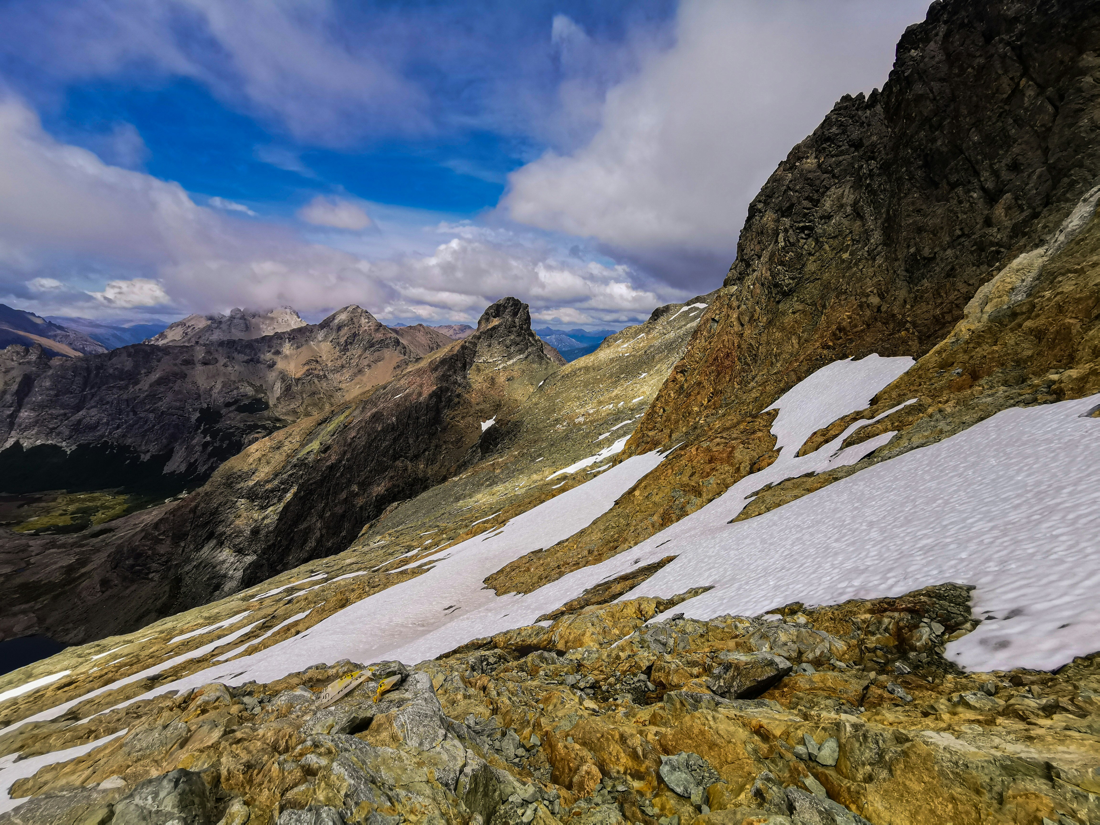 Mountain landscape with rocky peaks, patches of snow, and a dramatic sky.