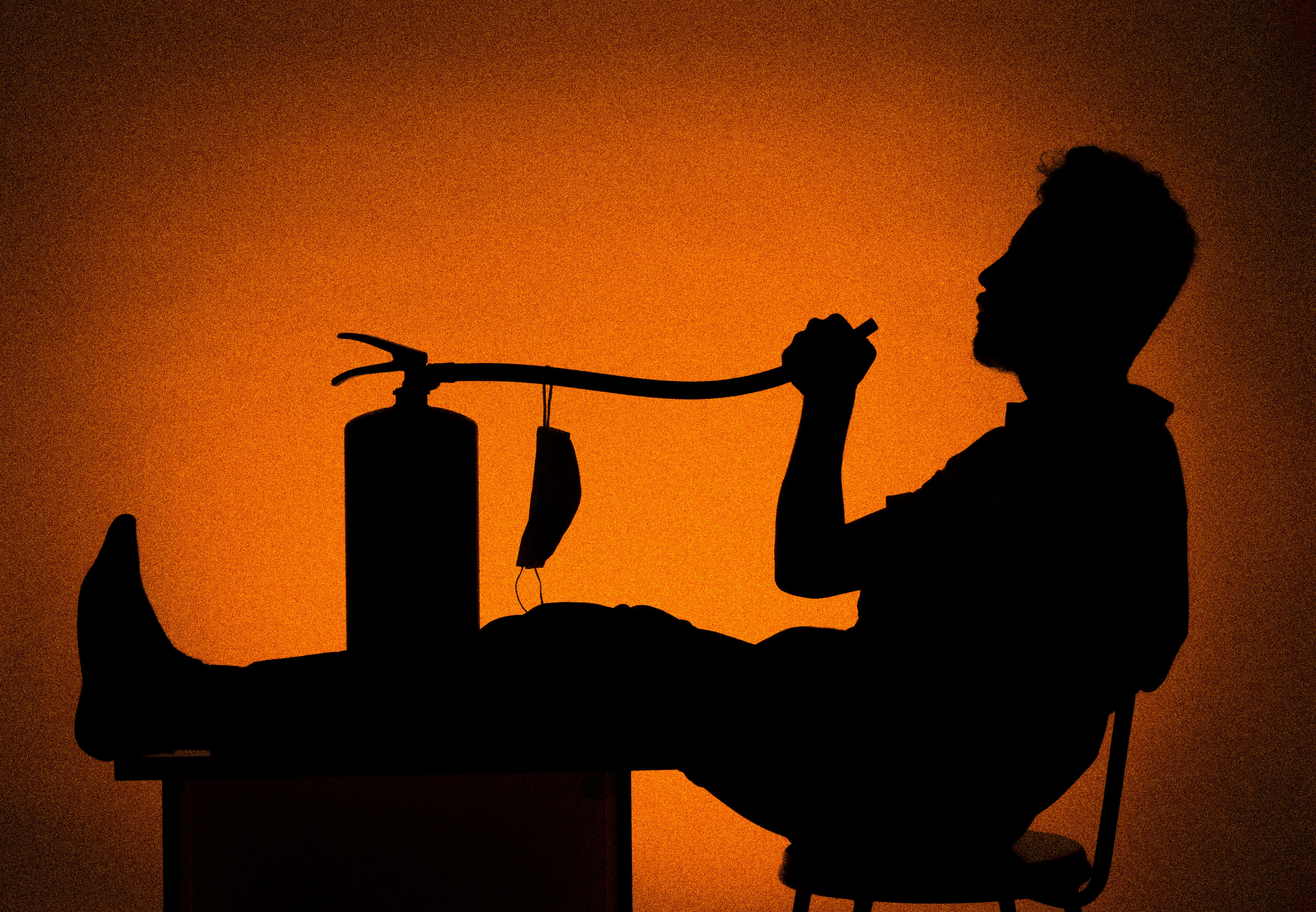 Silhouette of a person holding a fire extinguisher pipe against a vibrant orange backdrop.