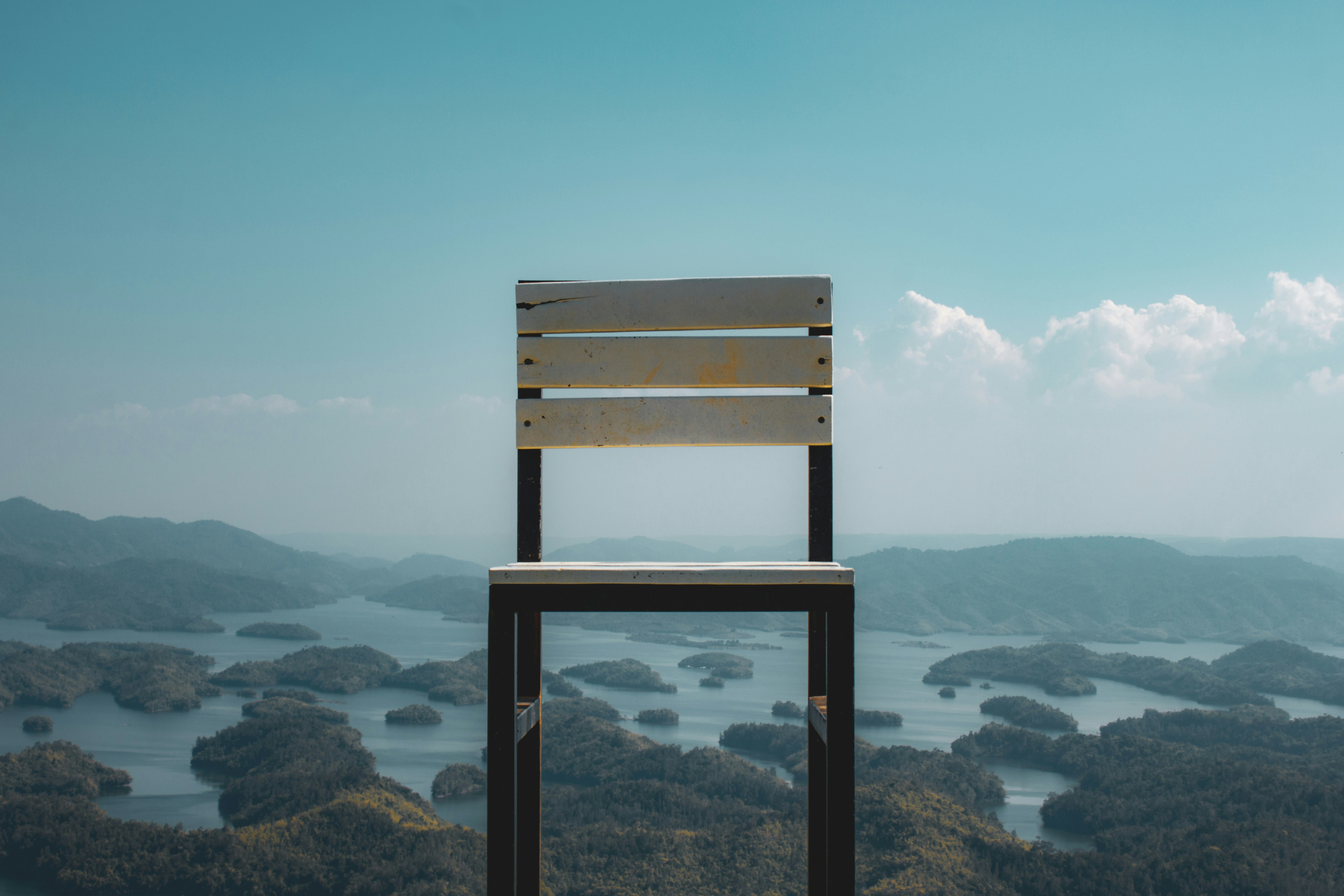 A minimalist chair stands alone against a backdrop of serene lakes and rolling hills, inviting contemplation. The scene captures the essence of solitude in nature.