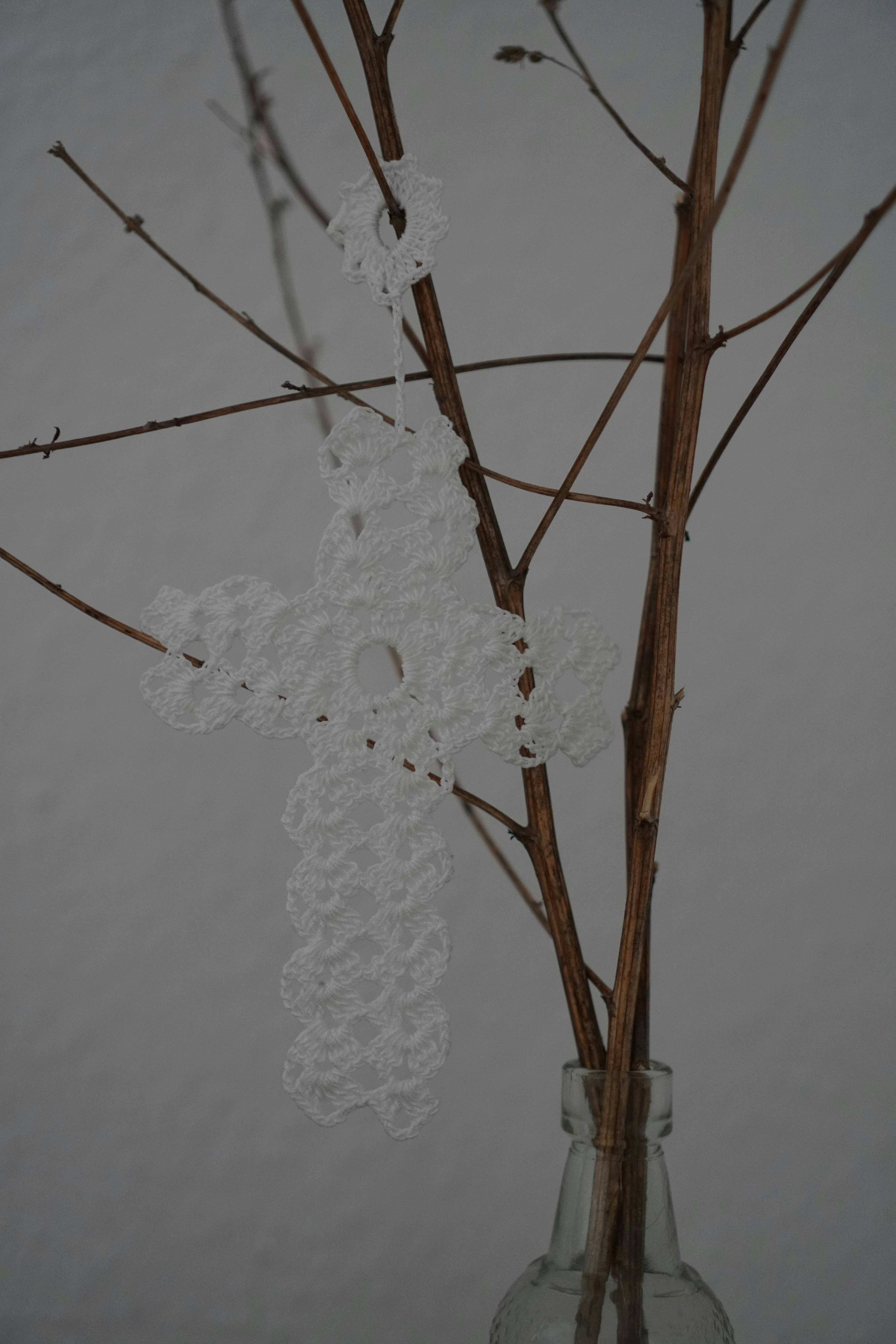 Crochet Cross Draped Over Bare Branches in a Glass Bottle: A Quiet Winter Still-Life