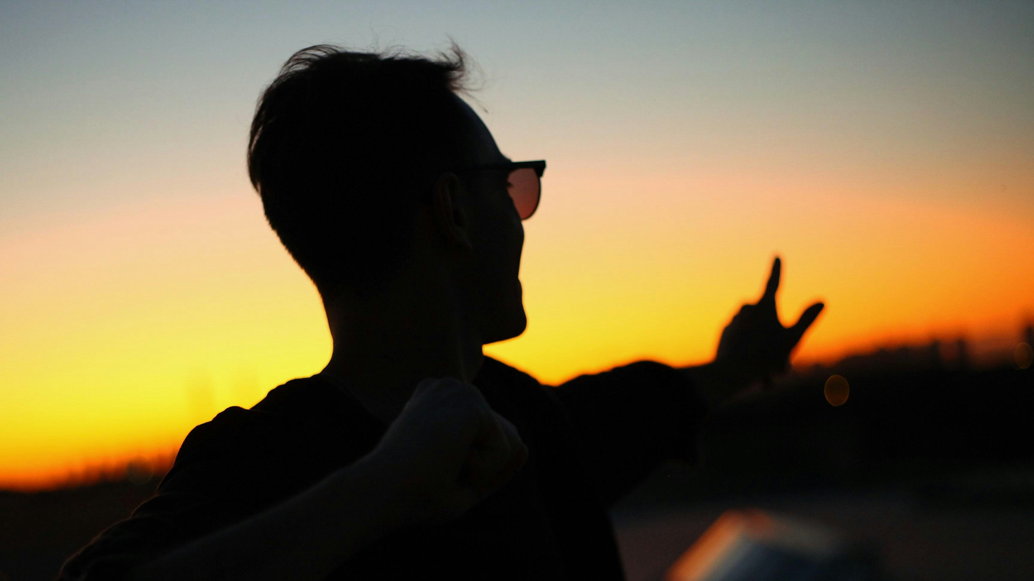 Silhouette of a person making a peace sign against a vibrant sunset sky.