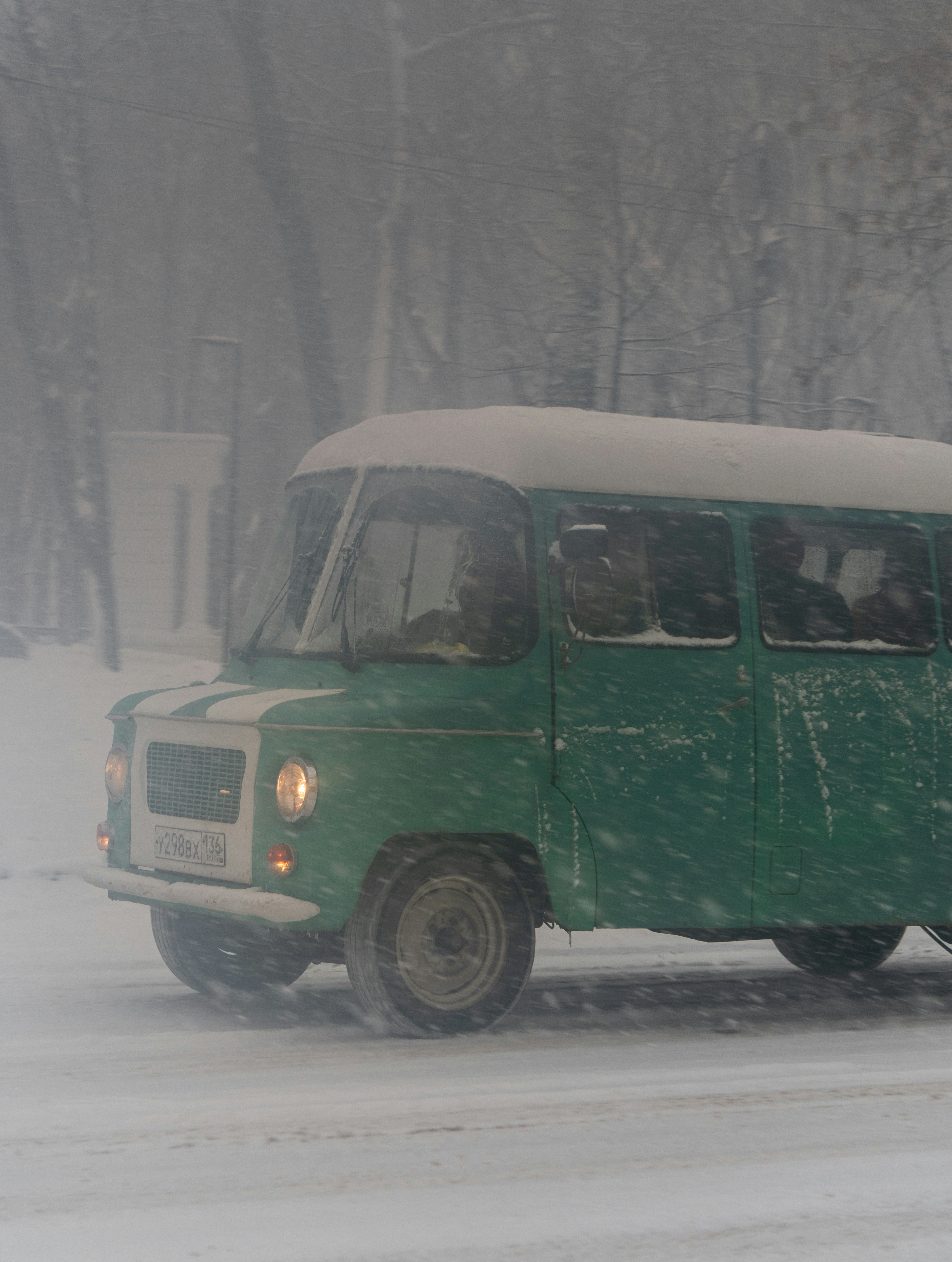 Vintage green van navigating through a snowy landscape, enveloped in a soft white haze. The scene captures the essence of winter travel.