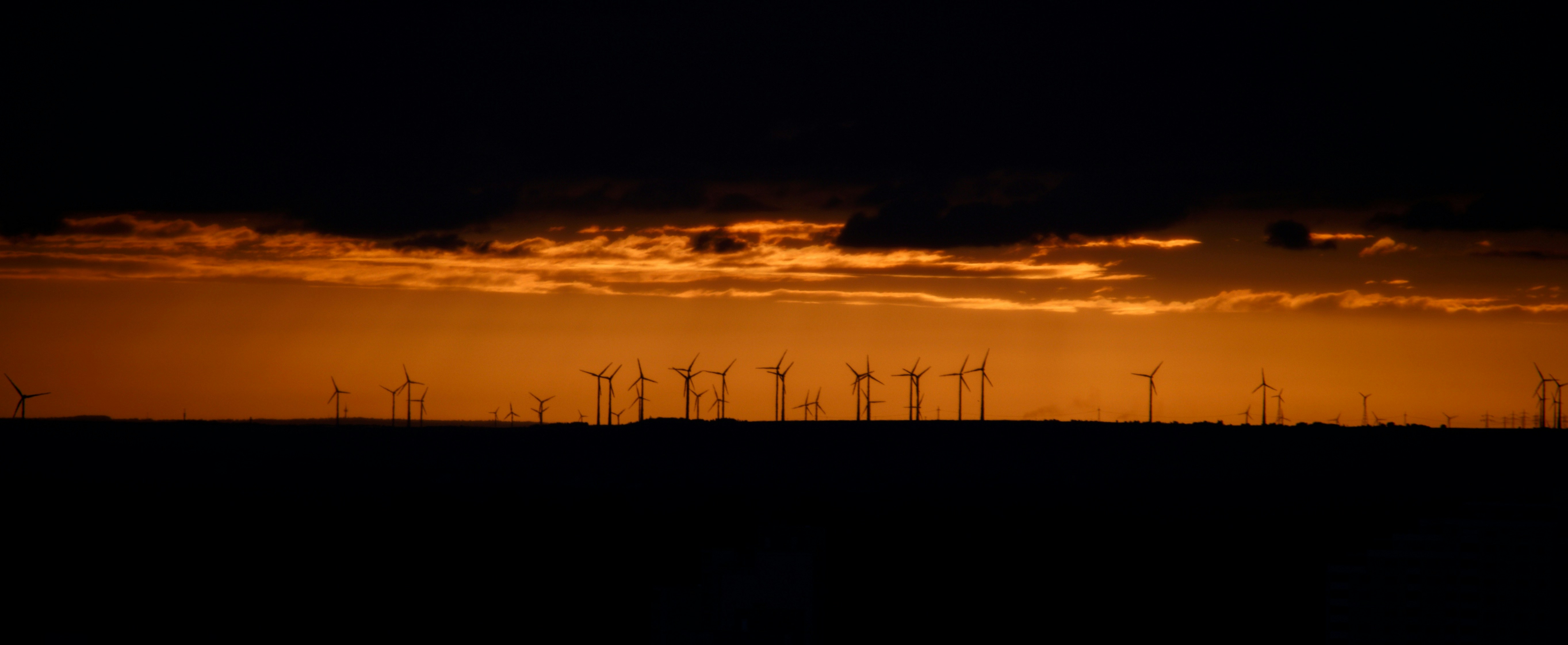 Silhouetted wind turbines against a vibrant sunset, casting a serene contrast between nature and technology.
