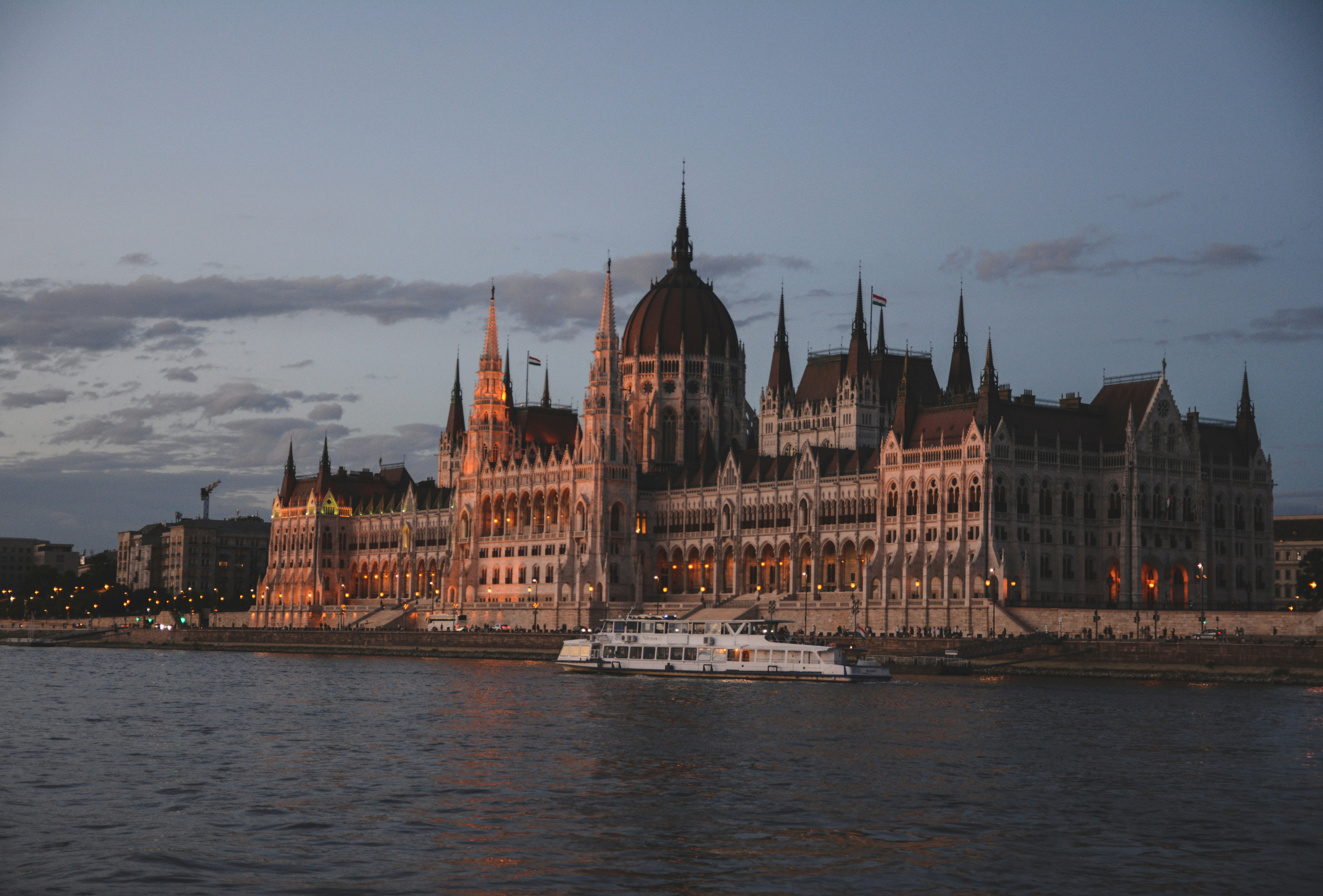 Hungarian Parliament Building illuminated at dusk with a boat passing on the Danube River.