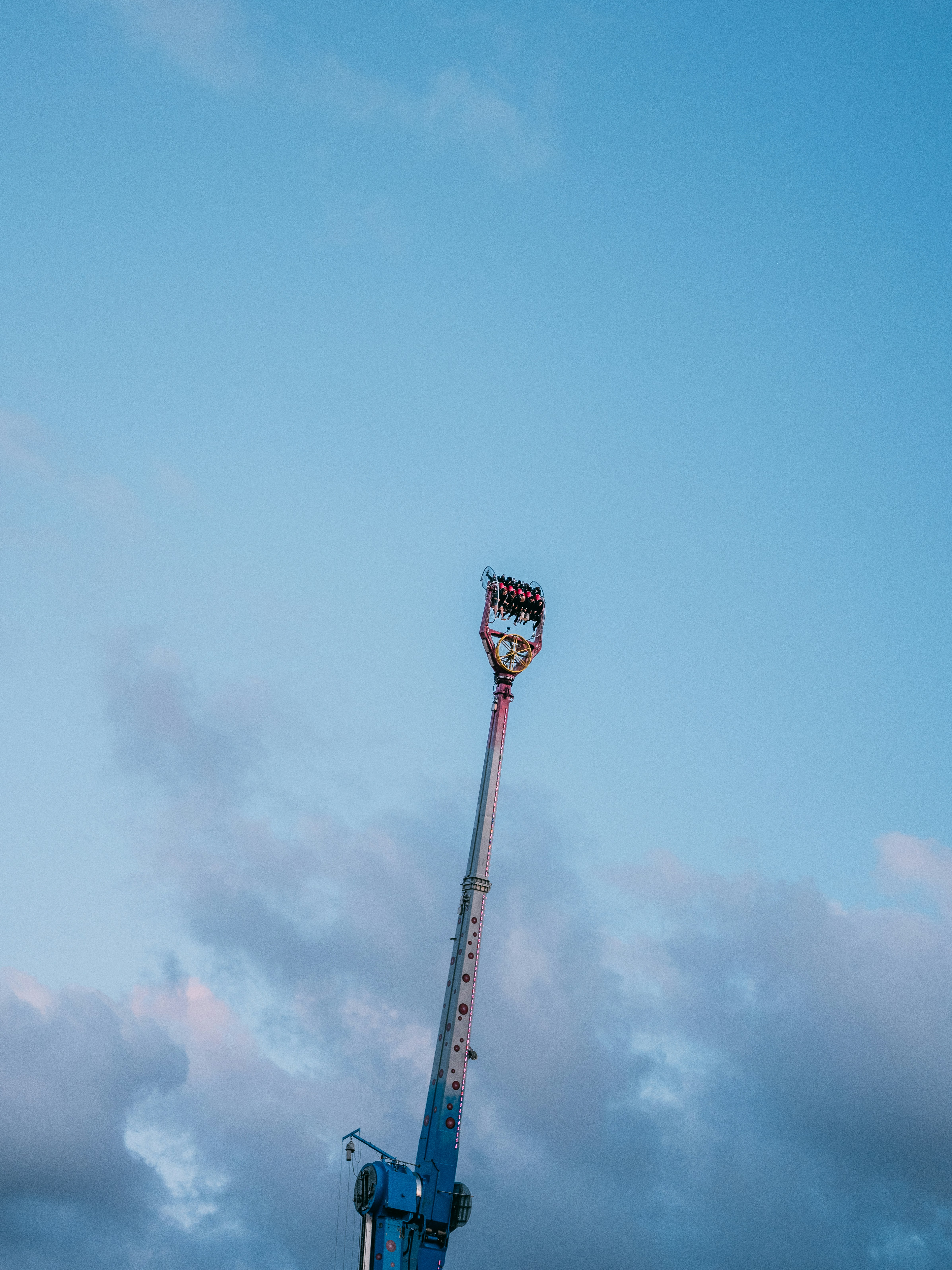A towering amusement ride reaching into the sky, with riders at the top against a backdrop of blue and cloudy sky.
