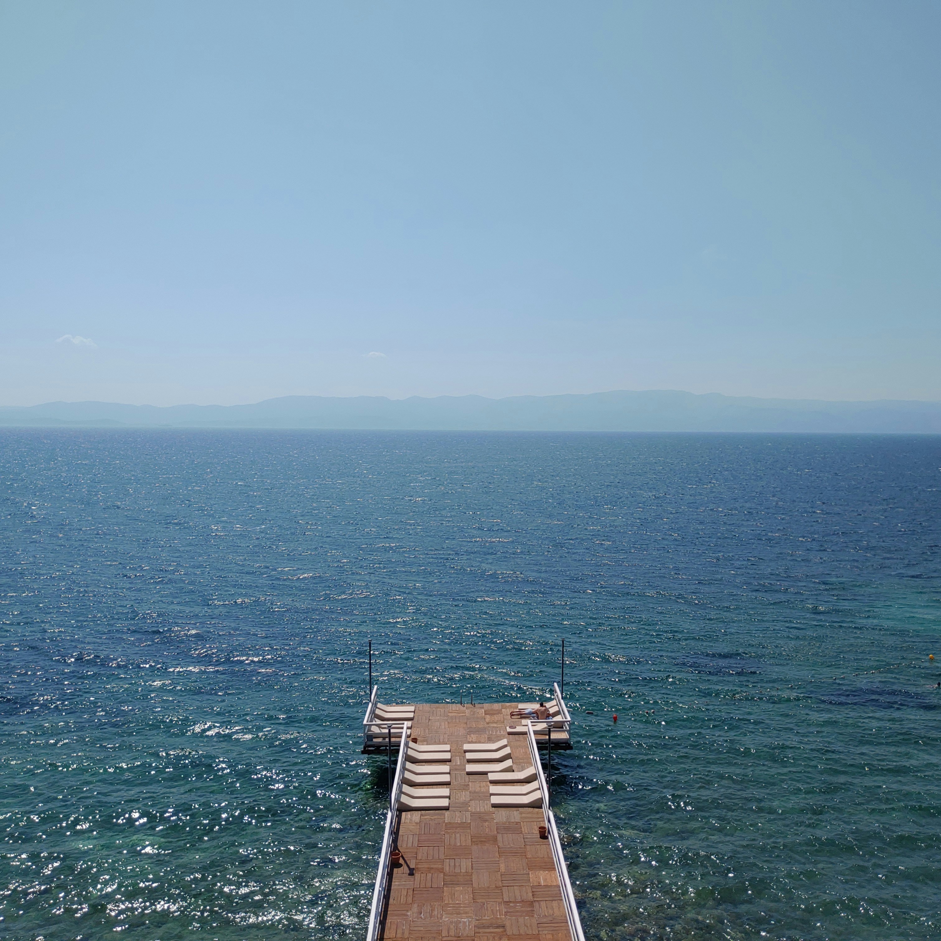 Wooden dock extending into a tranquil sea under a clear sky, inviting relaxation and reflection.
