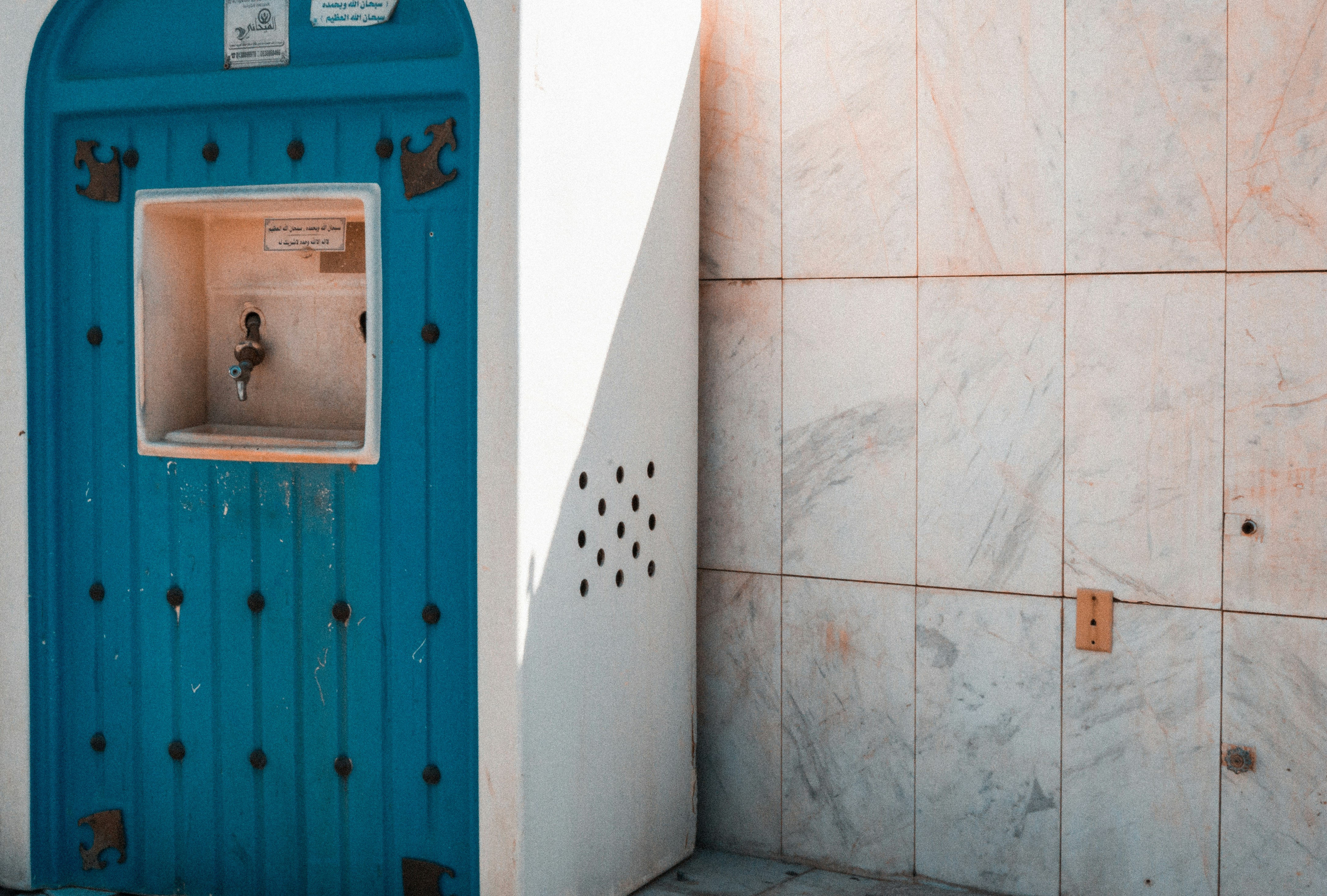 Bright blue water fountain against a textured marble wall, showcasing an intriguing blend of colors and materials.