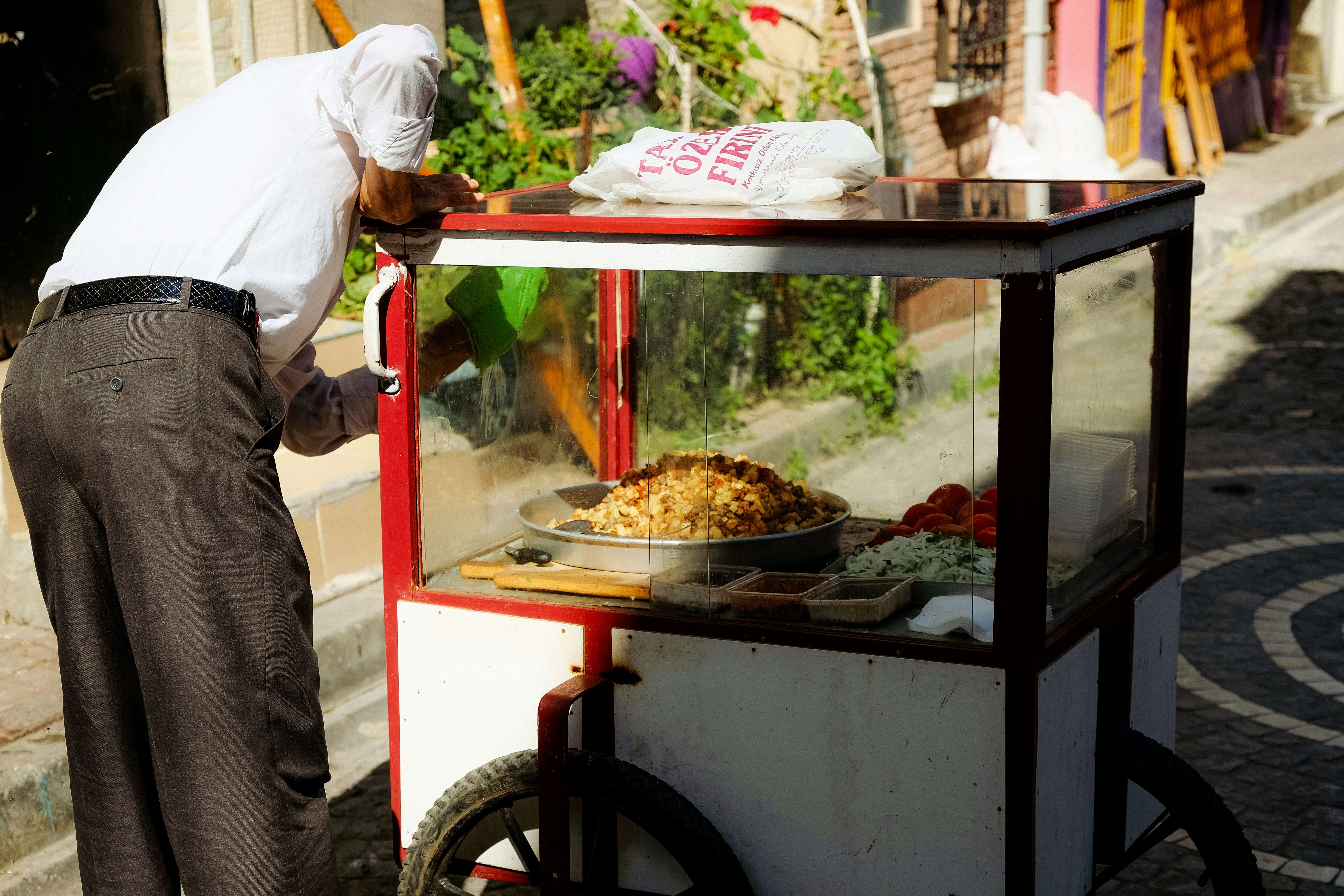 Sunlit Sizzle: Street Vendor at Glass-front Cart
