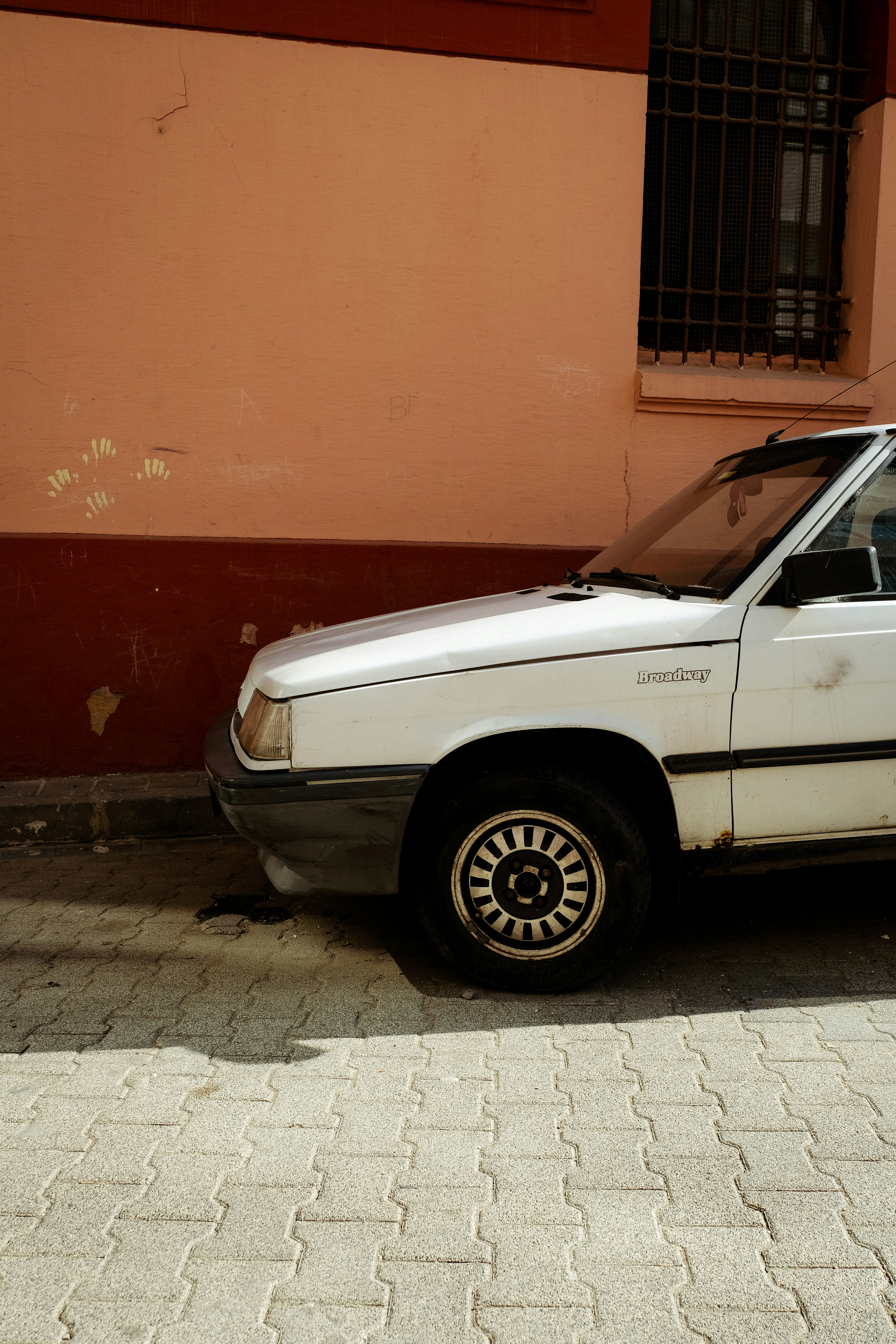 Sunlit Street Portrait: A Weathered White Sedan by a Peach Wall