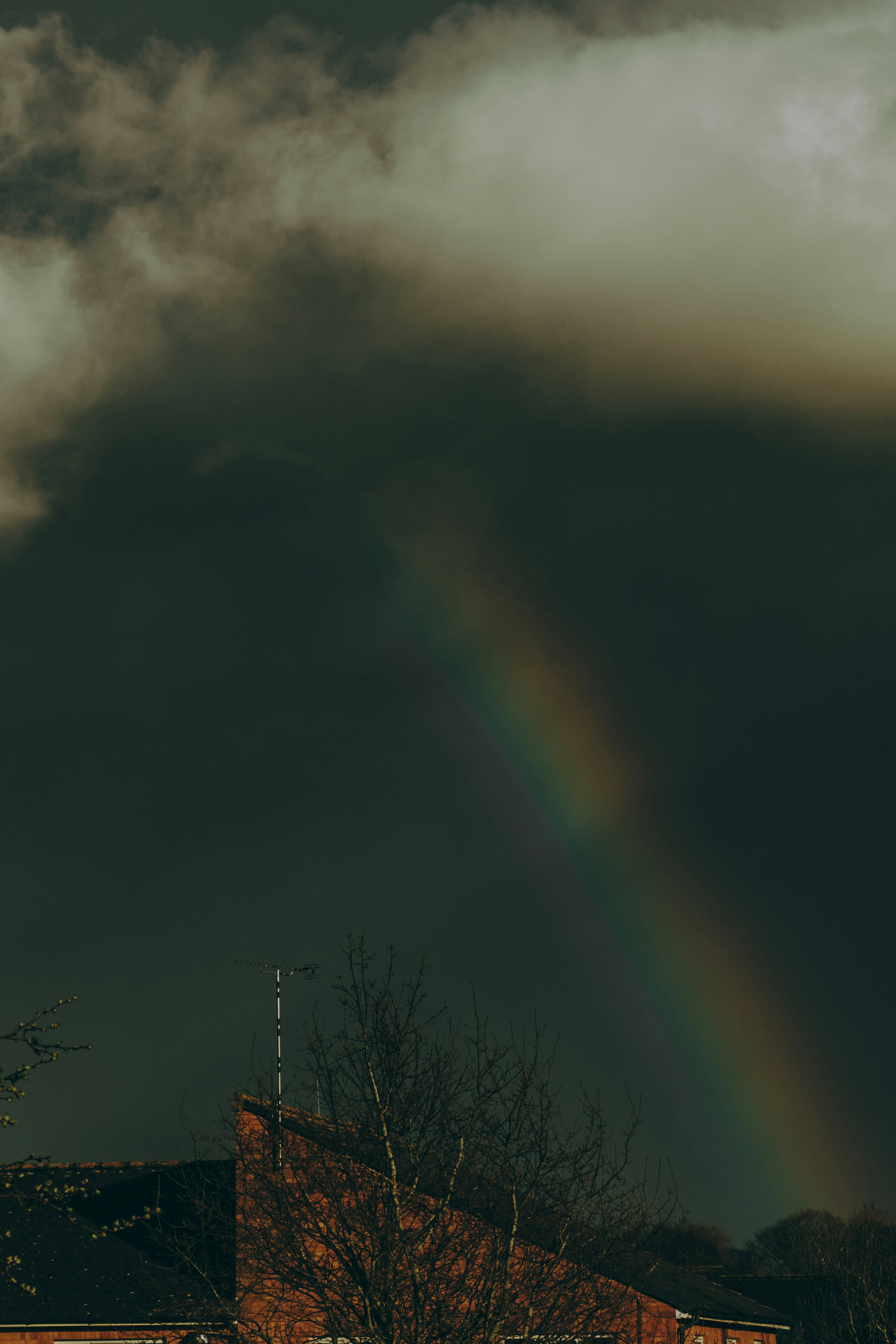 Rainbow Arc Over Brick Rooftops Beneath a Looming Dusk Sky