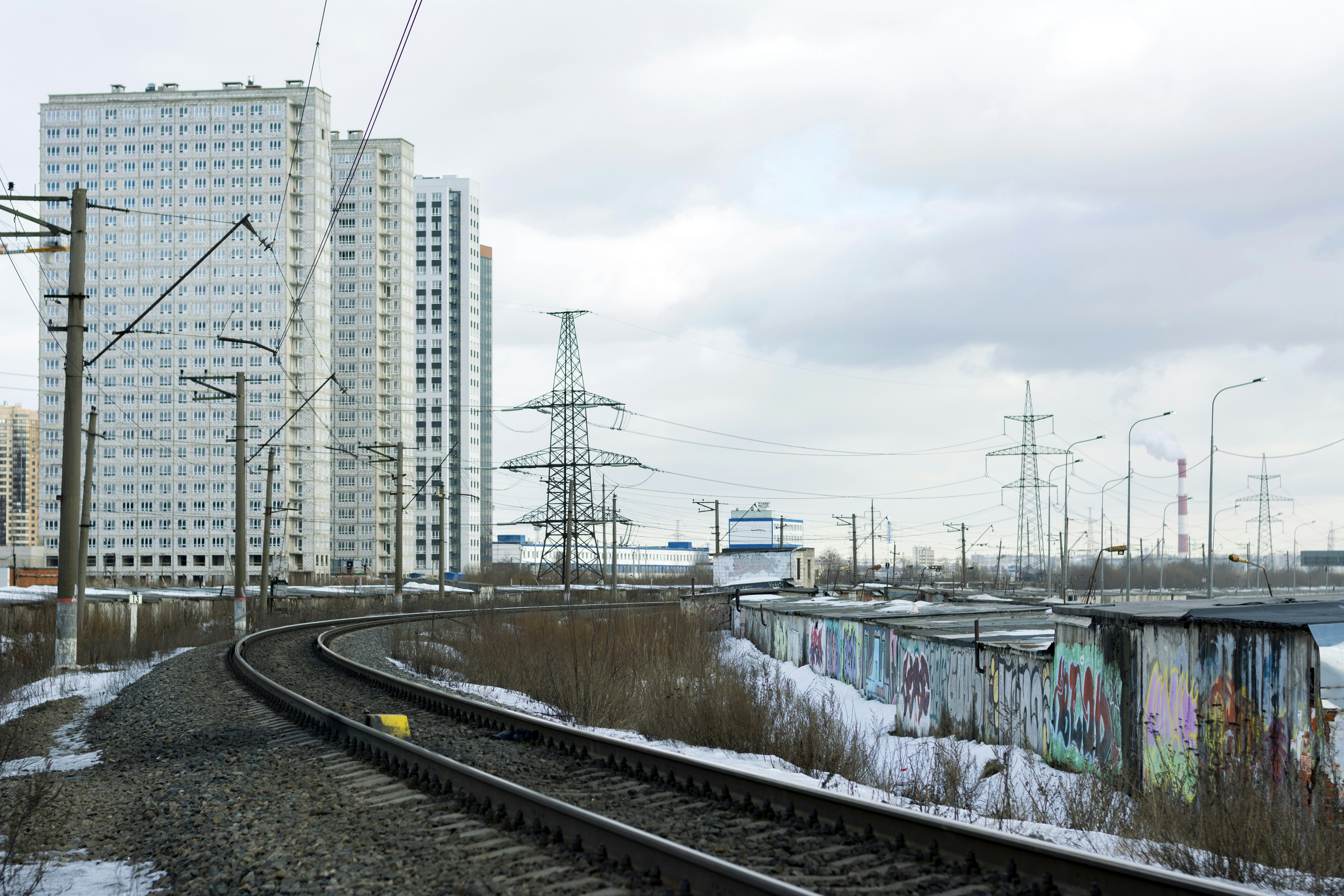 Rails Curve through a Graffiti Barrier under a Winter Gray Sky