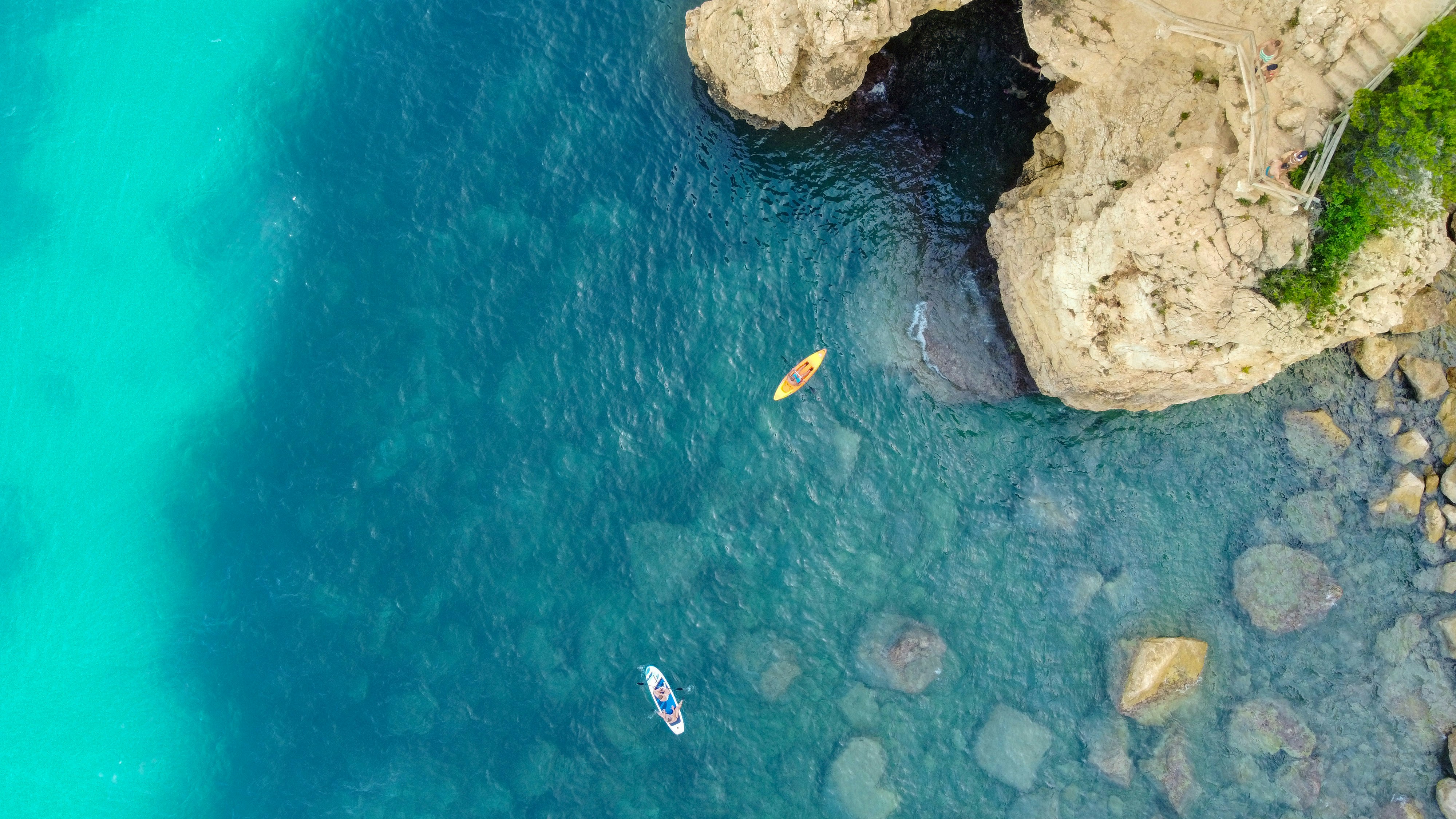 Kayaks gliding through clear turquoise waters near a rocky coastline.