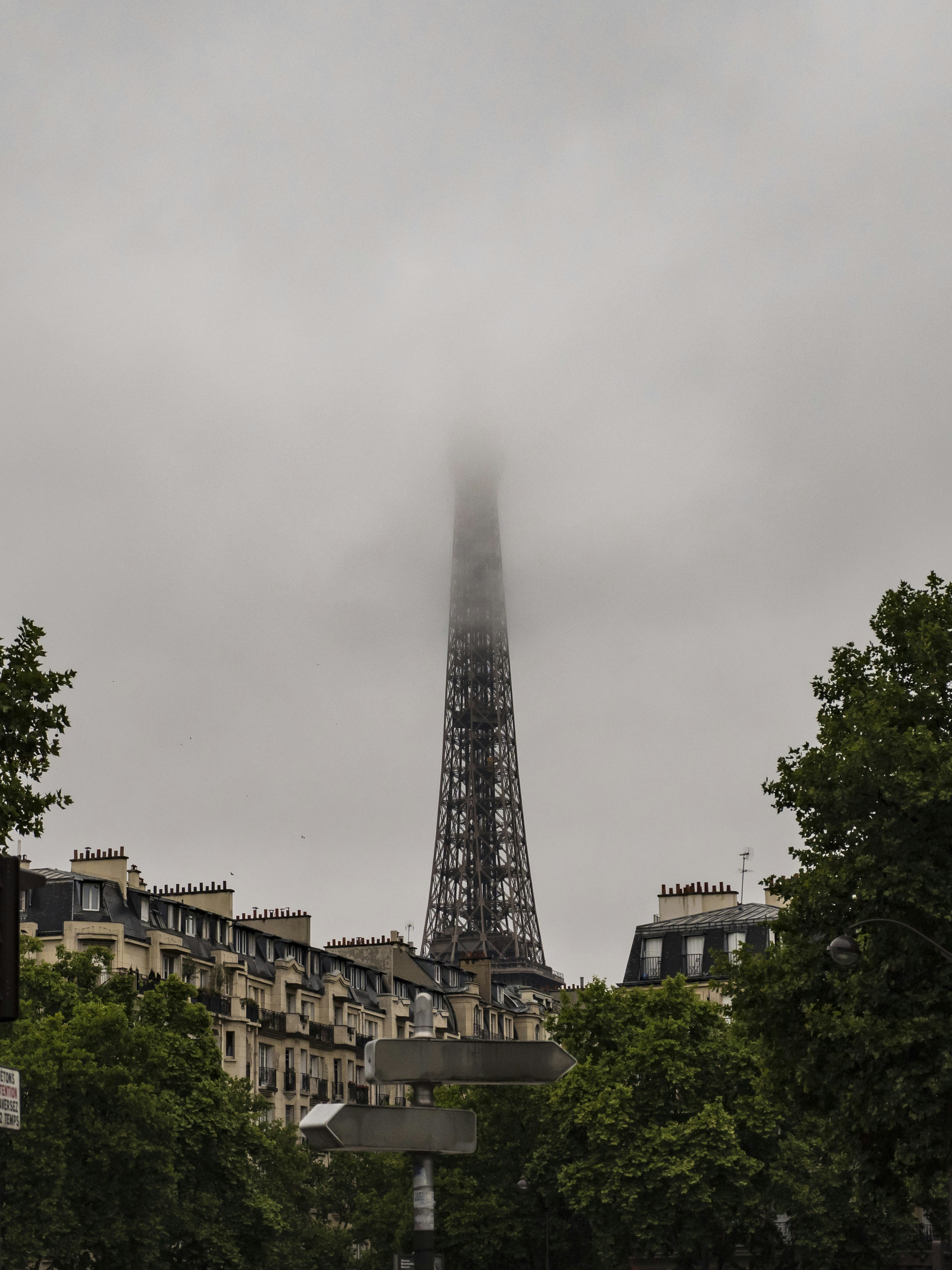 Eiffel Tower partially obscured by thick fog, surrounded by Parisian architecture and lush greenery.