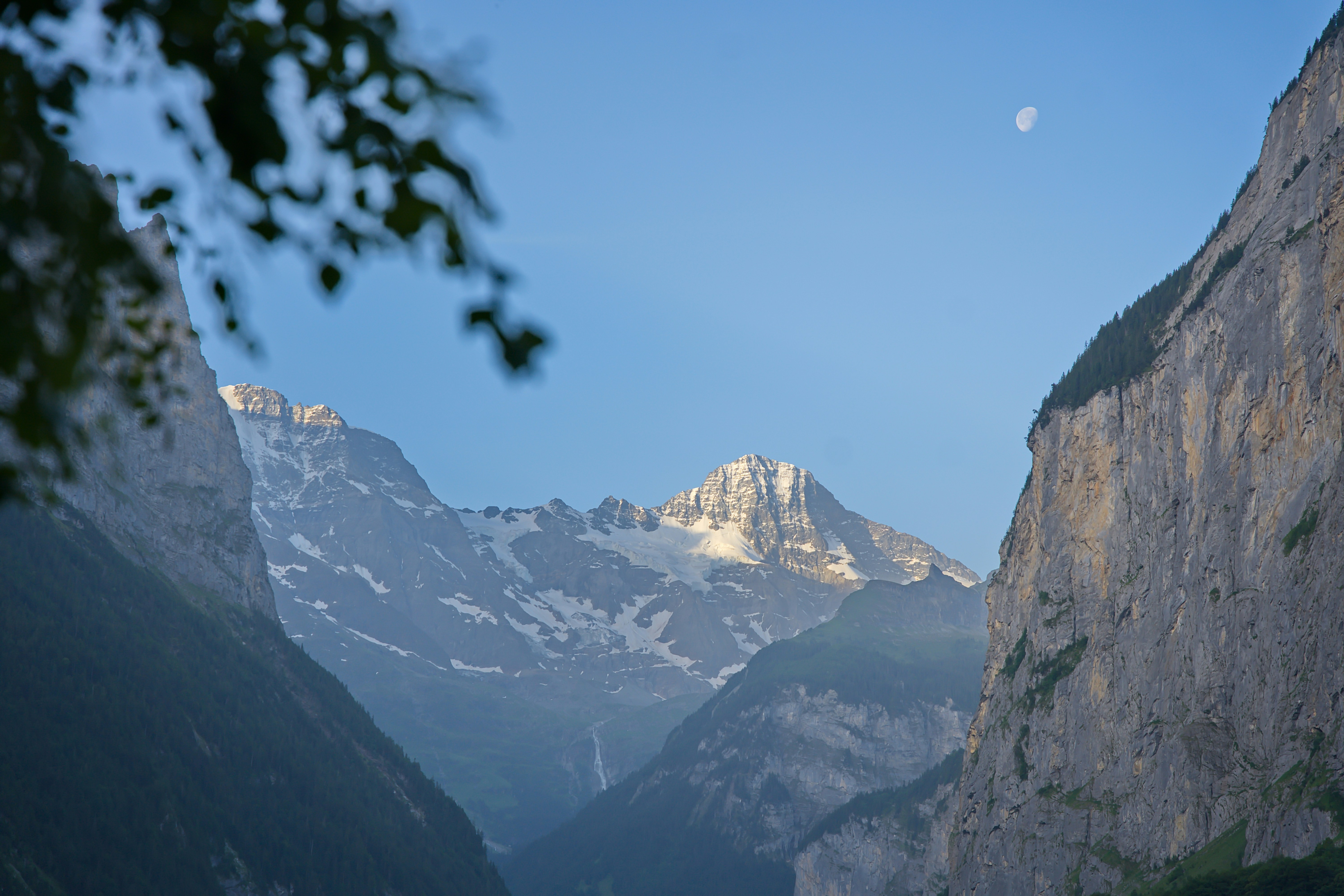 Crescent Moon Over Sunlit Peaks Framed by a Narrow Alpine Gorge