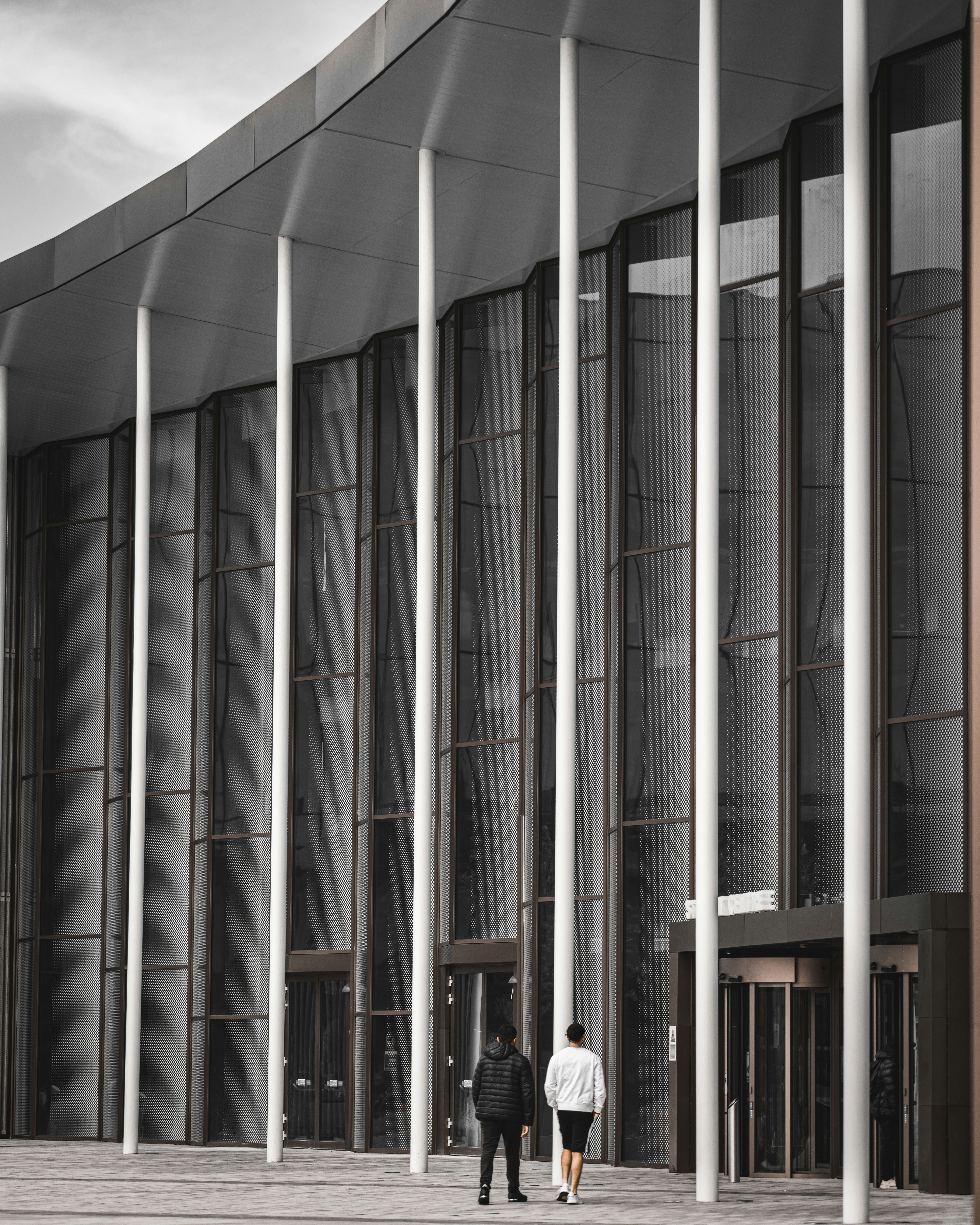 Two figures walking towards a sleek, modern building with striking vertical lines and glass facades.