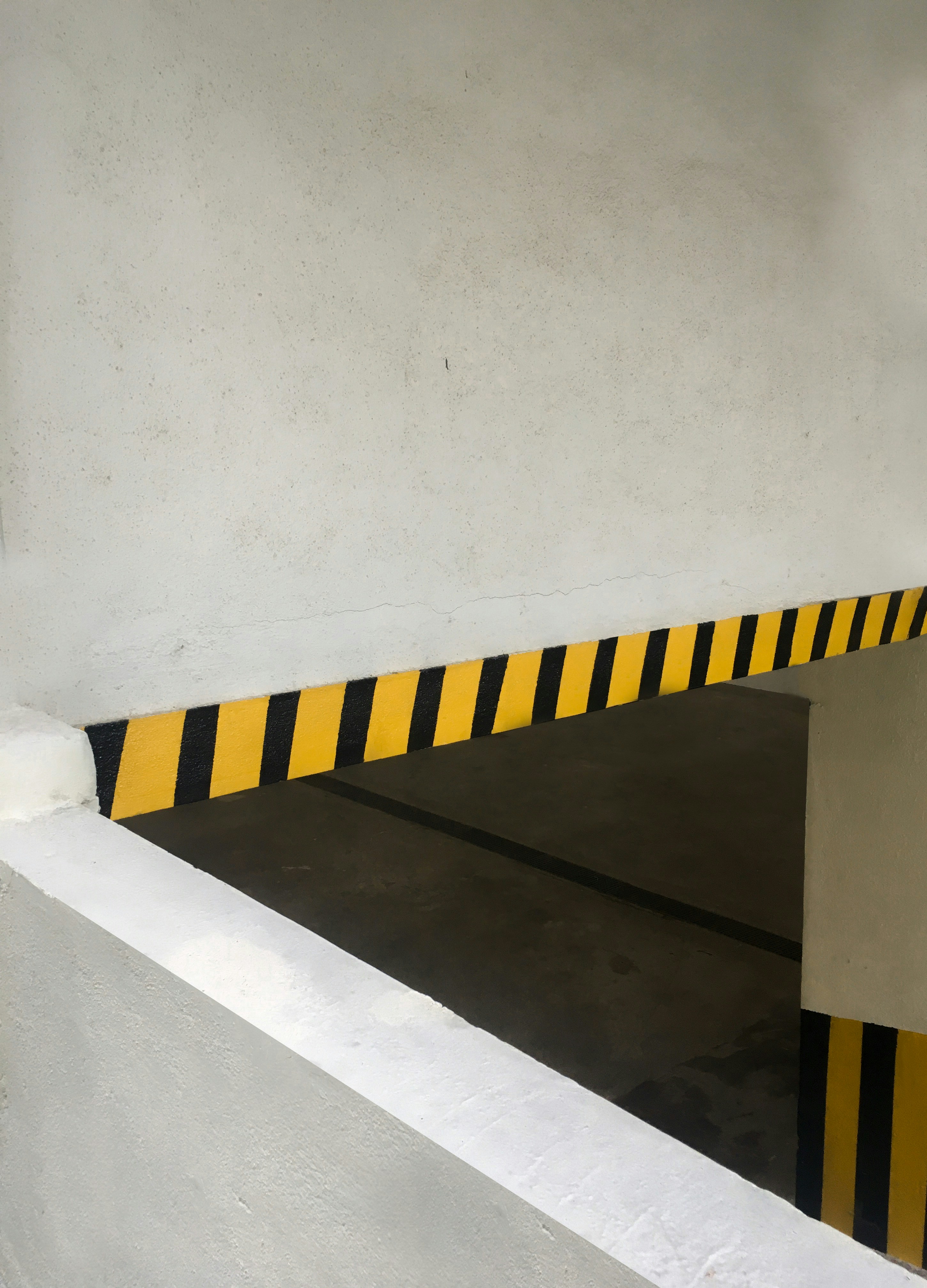 Yellow and black striped safety markings on a white wall corner in a parking structure, emphasizing spatial boundaries.