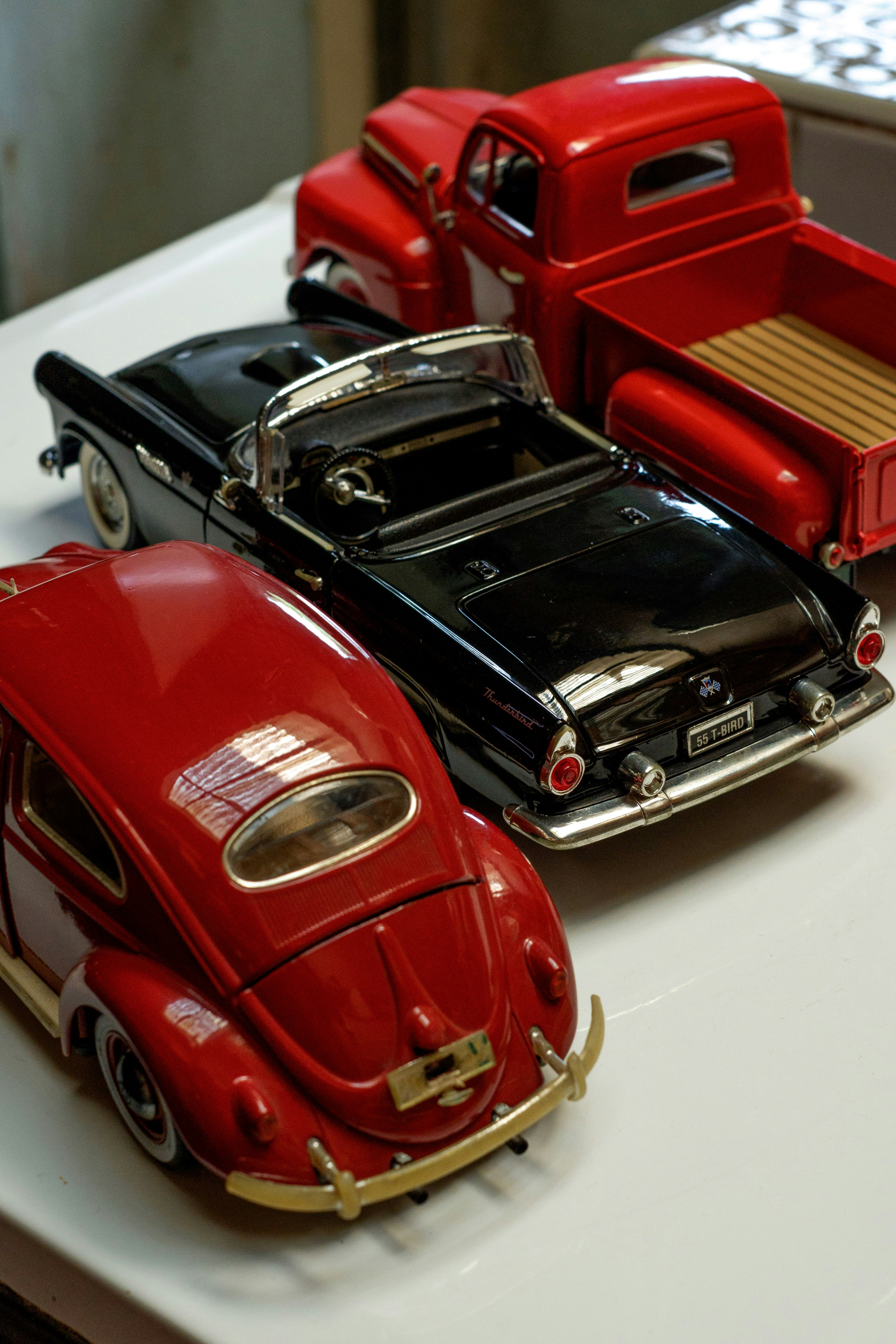 Close-up photograph of miniature toy cars arranged on a white tray. The black vintage convertible sits among red vehicles, chrome details catching the light.
