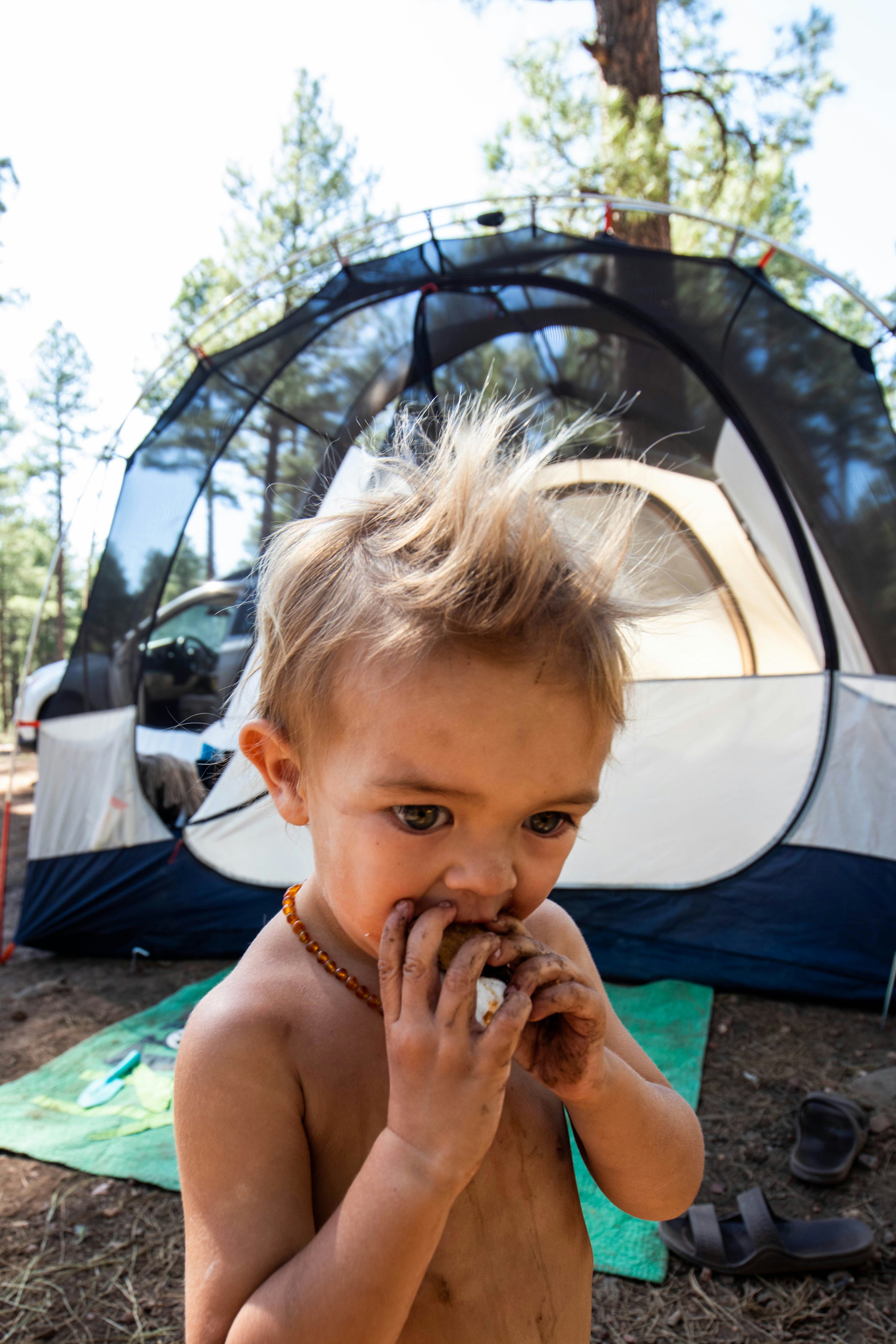 Young child enjoying a messy snack outdoors in front of a camping tent. The scene captures the essence of childhood joy and outdoor adventure.
