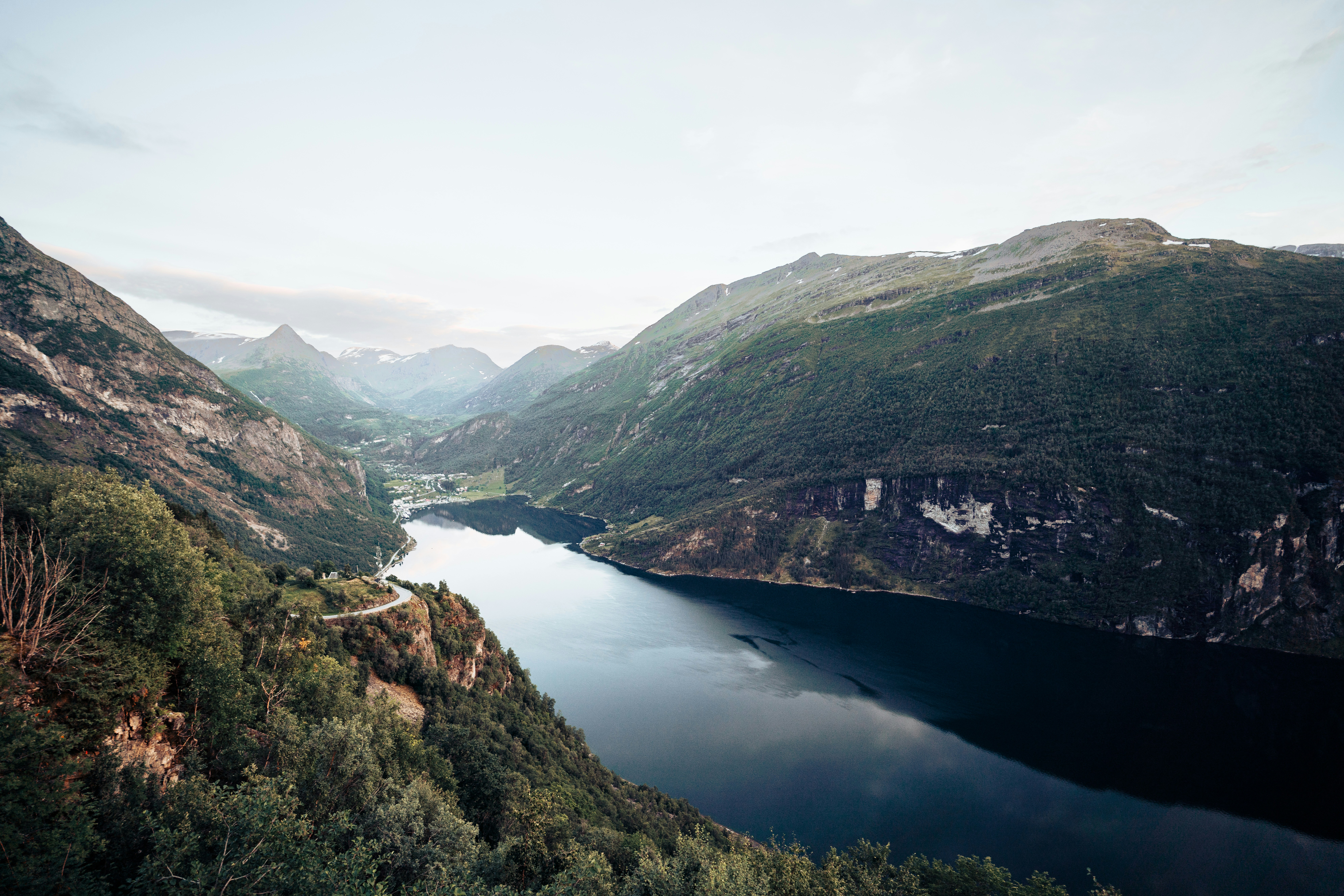 Deep blue fjord flanked by lush green mountains under a soft sky.