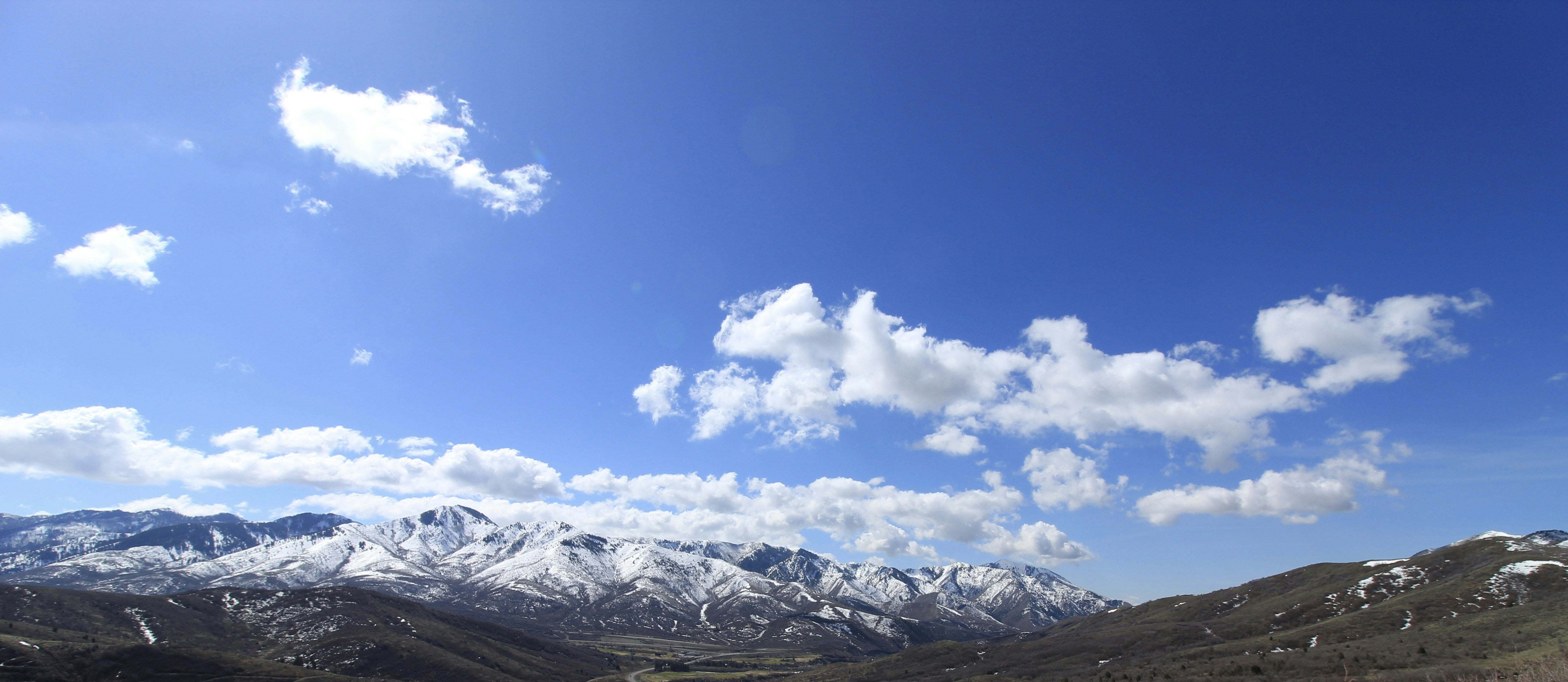 Snow-capped mountains stretch across a clear blue sky, punctuated by fluffy clouds. The serene landscape captures the tranquility of winter.