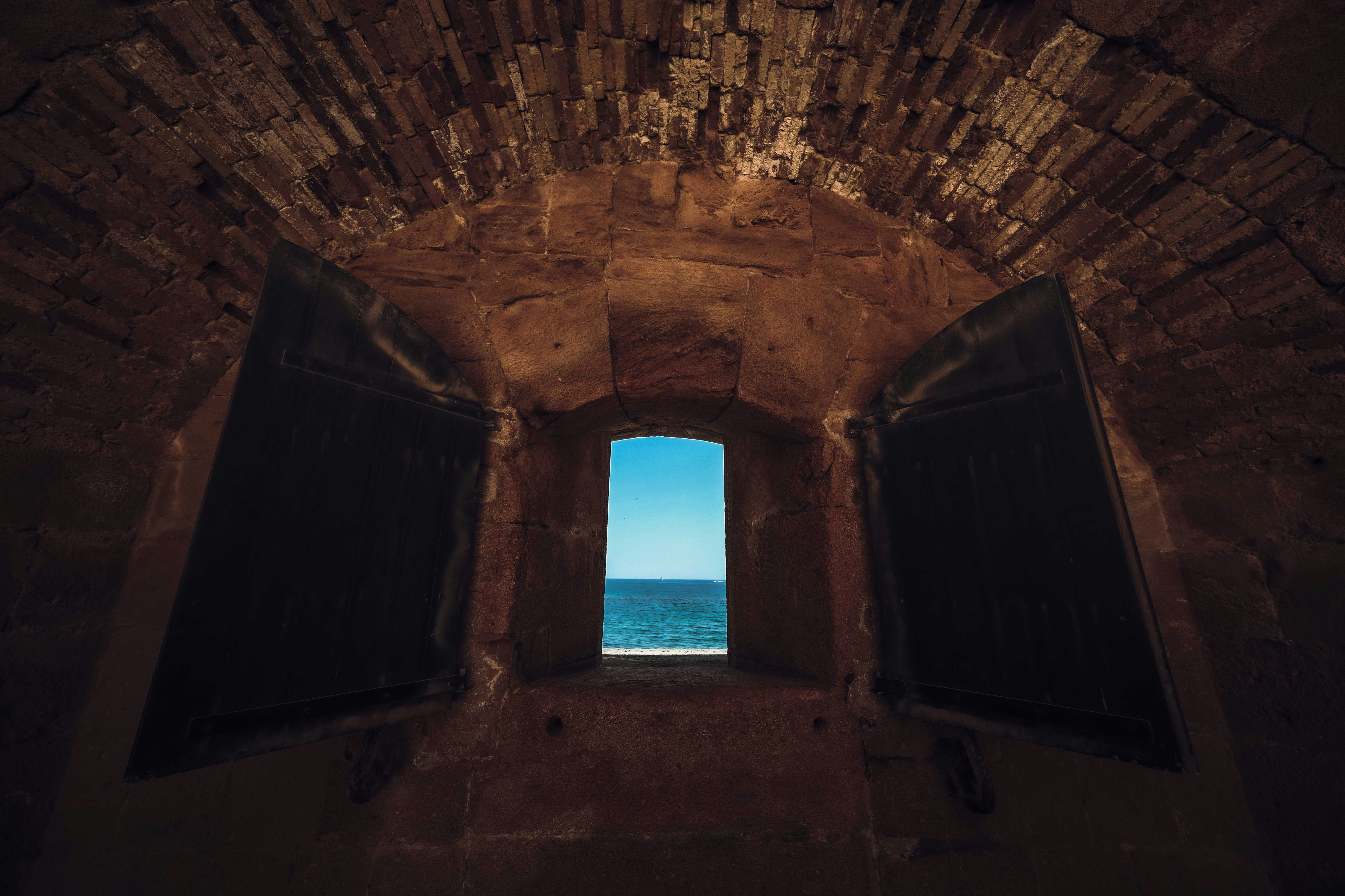 Stone-walled alcove framing a bright blue ocean view through a central window.